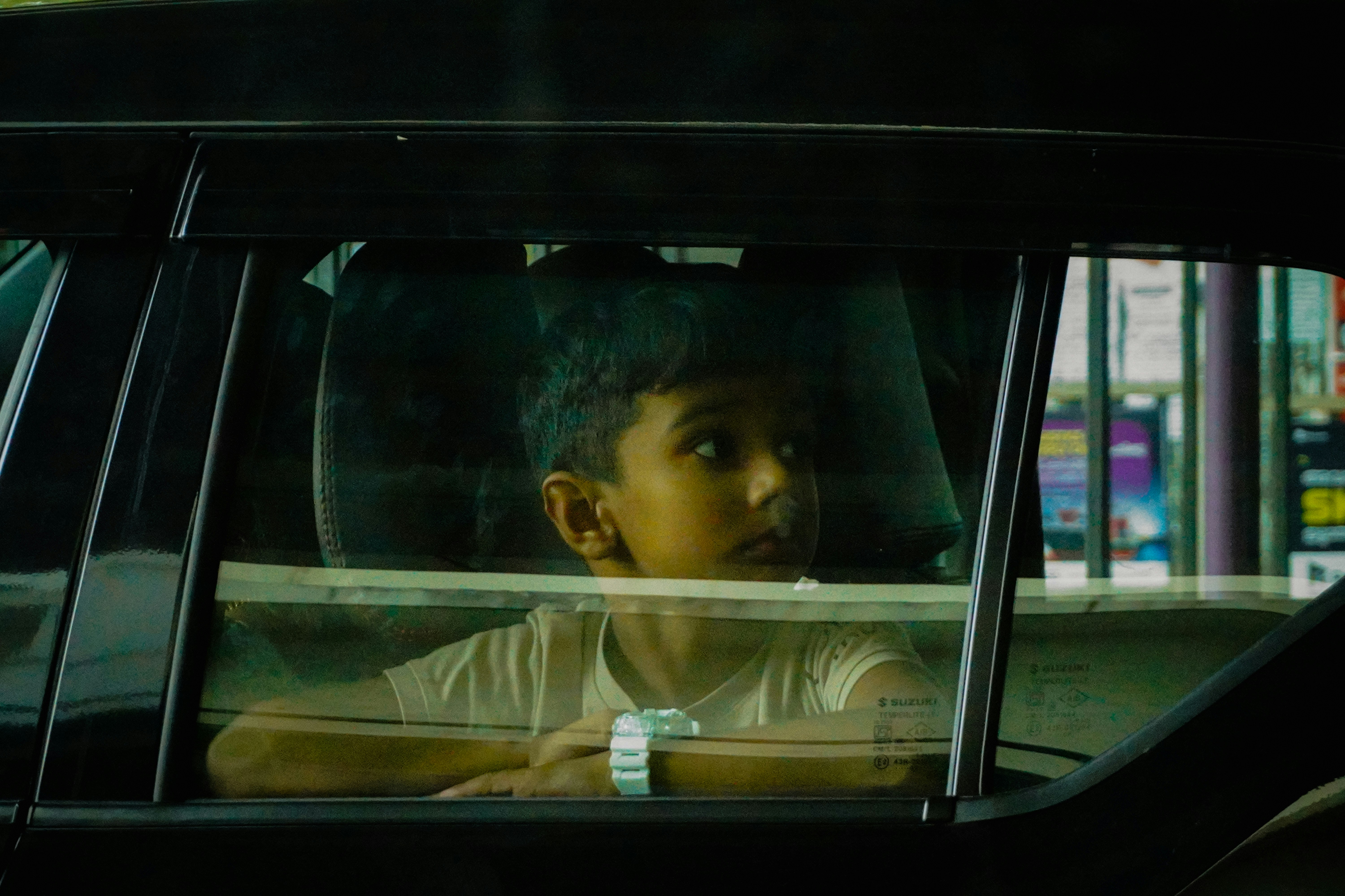 A young boy looks out a dark car window.