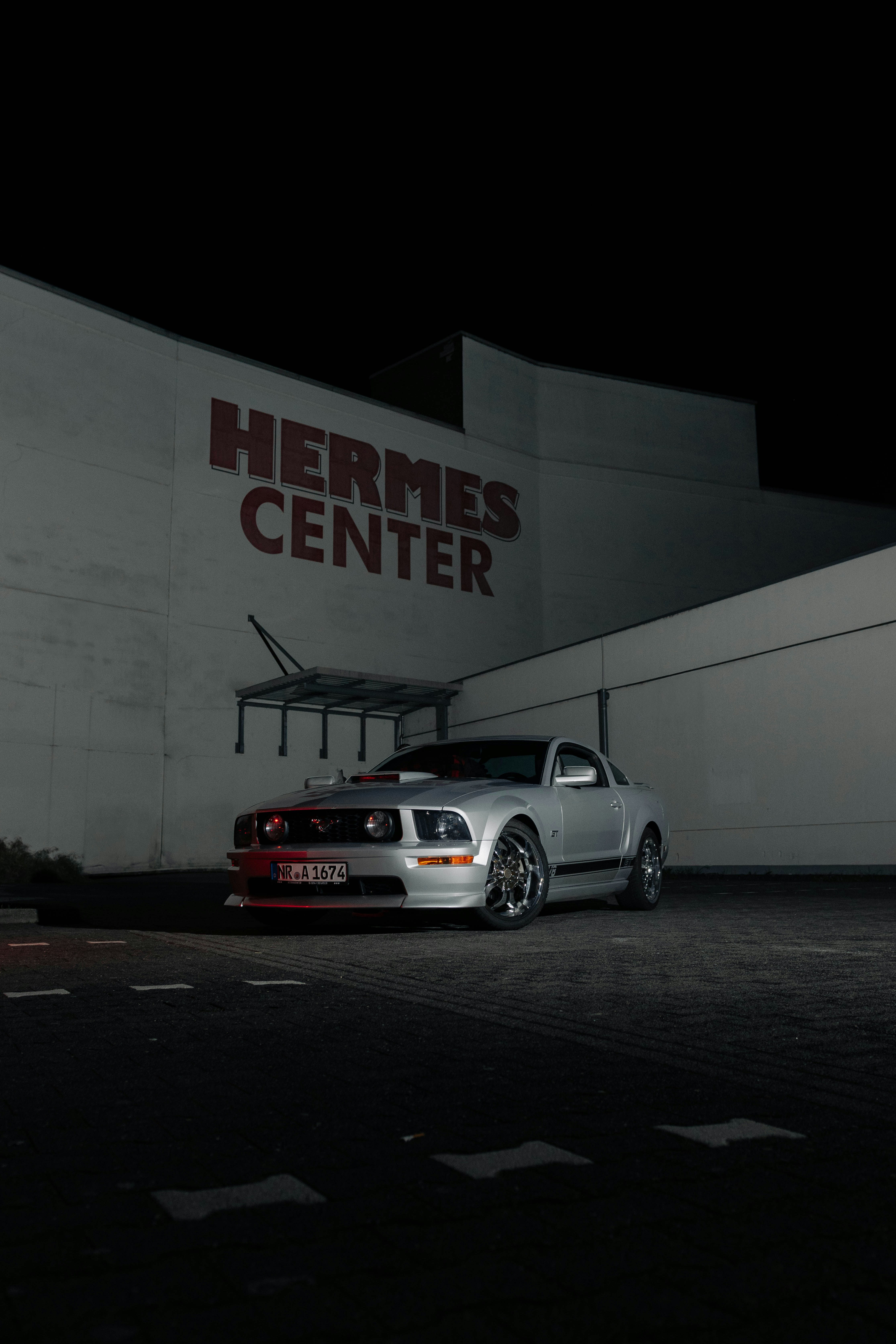 White Mustang under Hermes Center Sign at Night