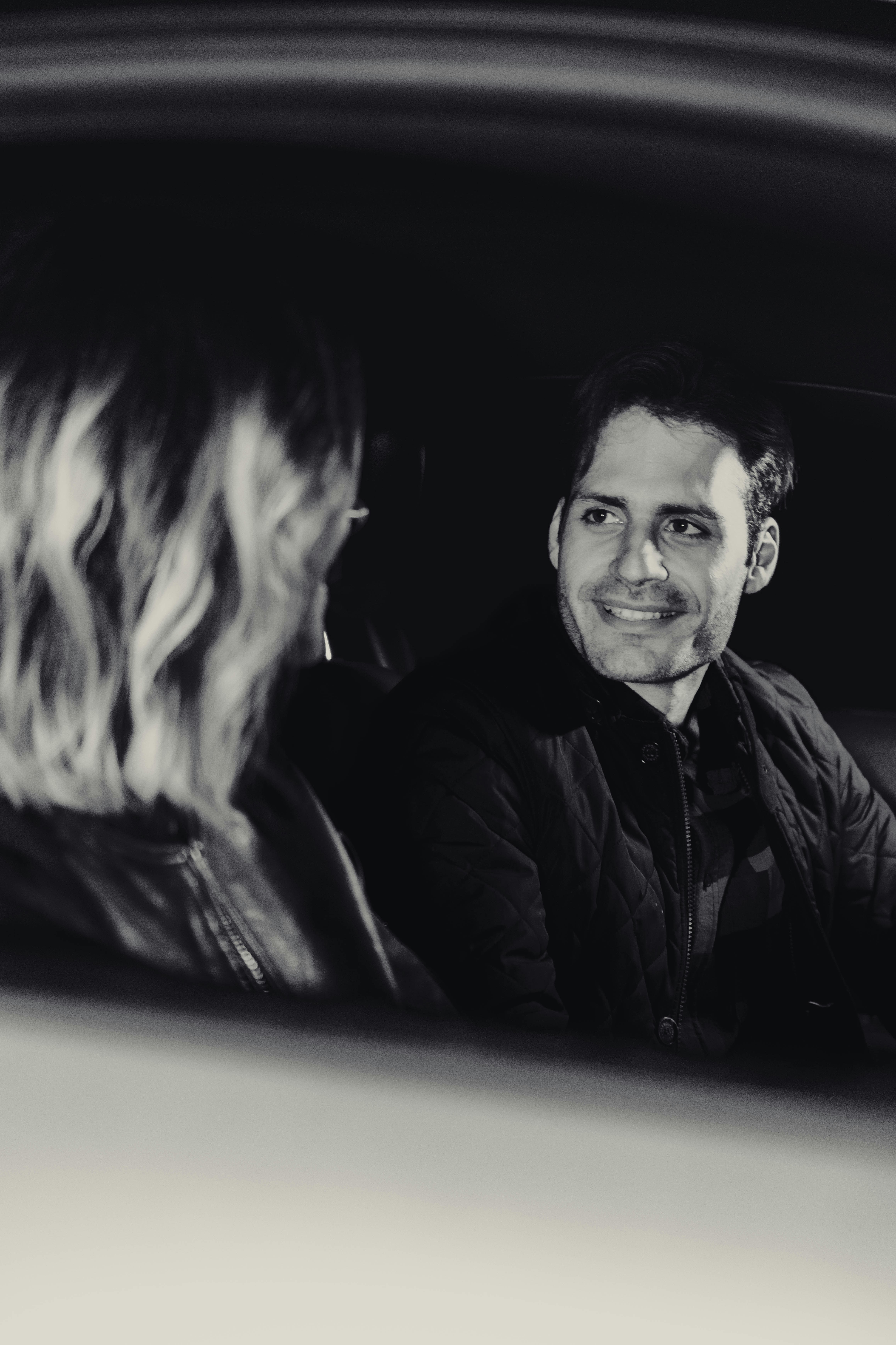 Man smiling at woman in car, black and white.