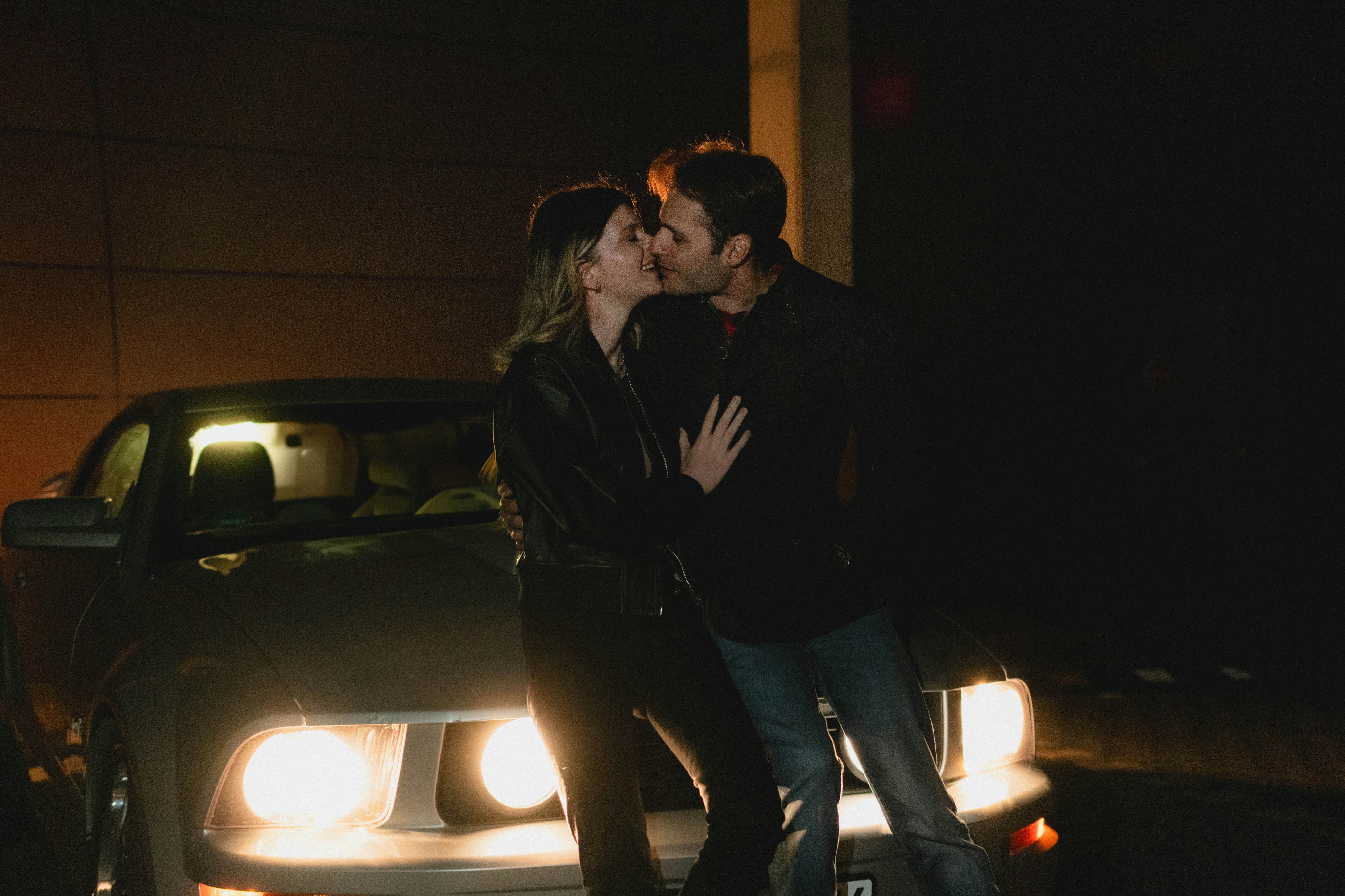 A couple kissing passionately next to a car at night.