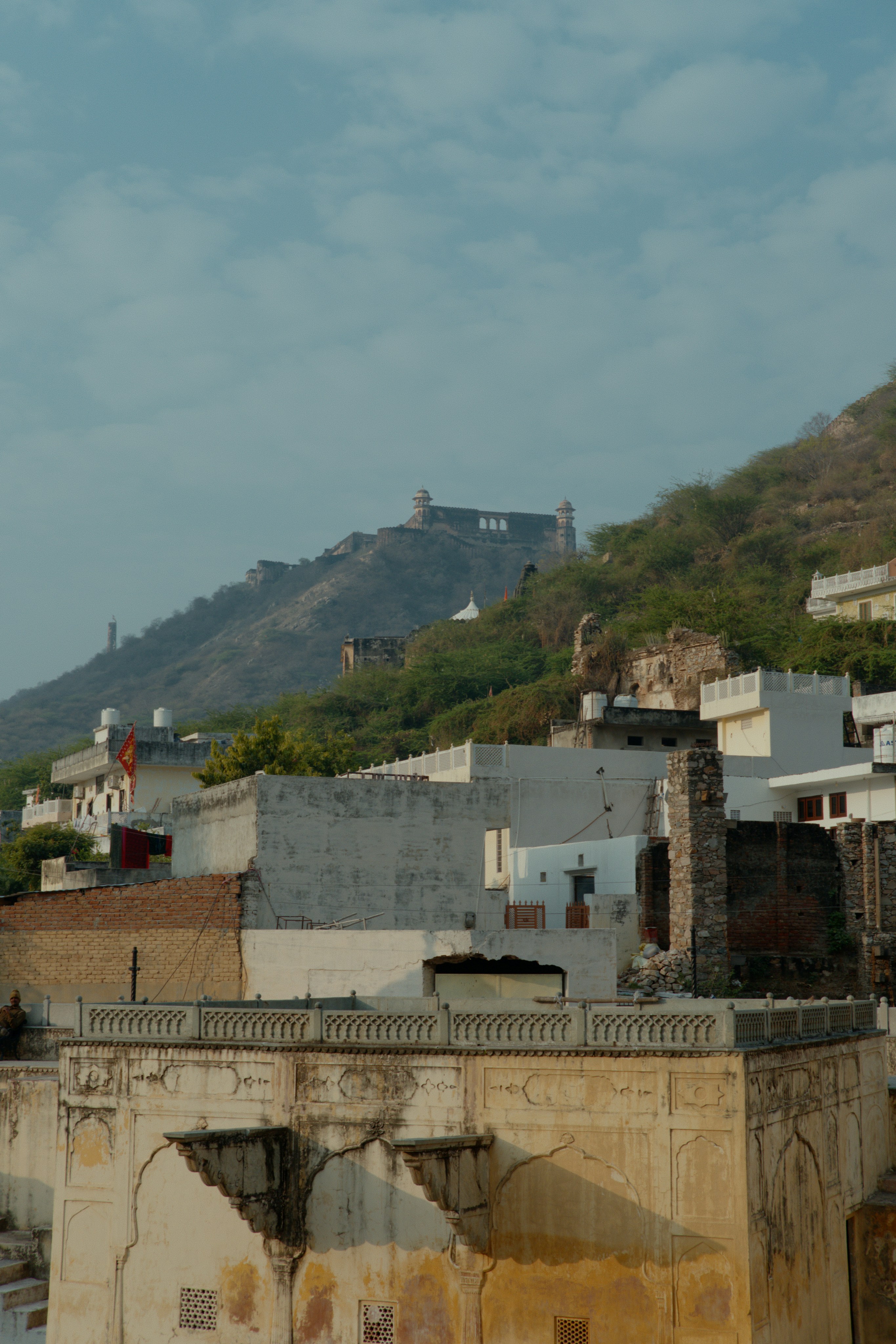 Ancient fort overlooks hillside village with various buildings.