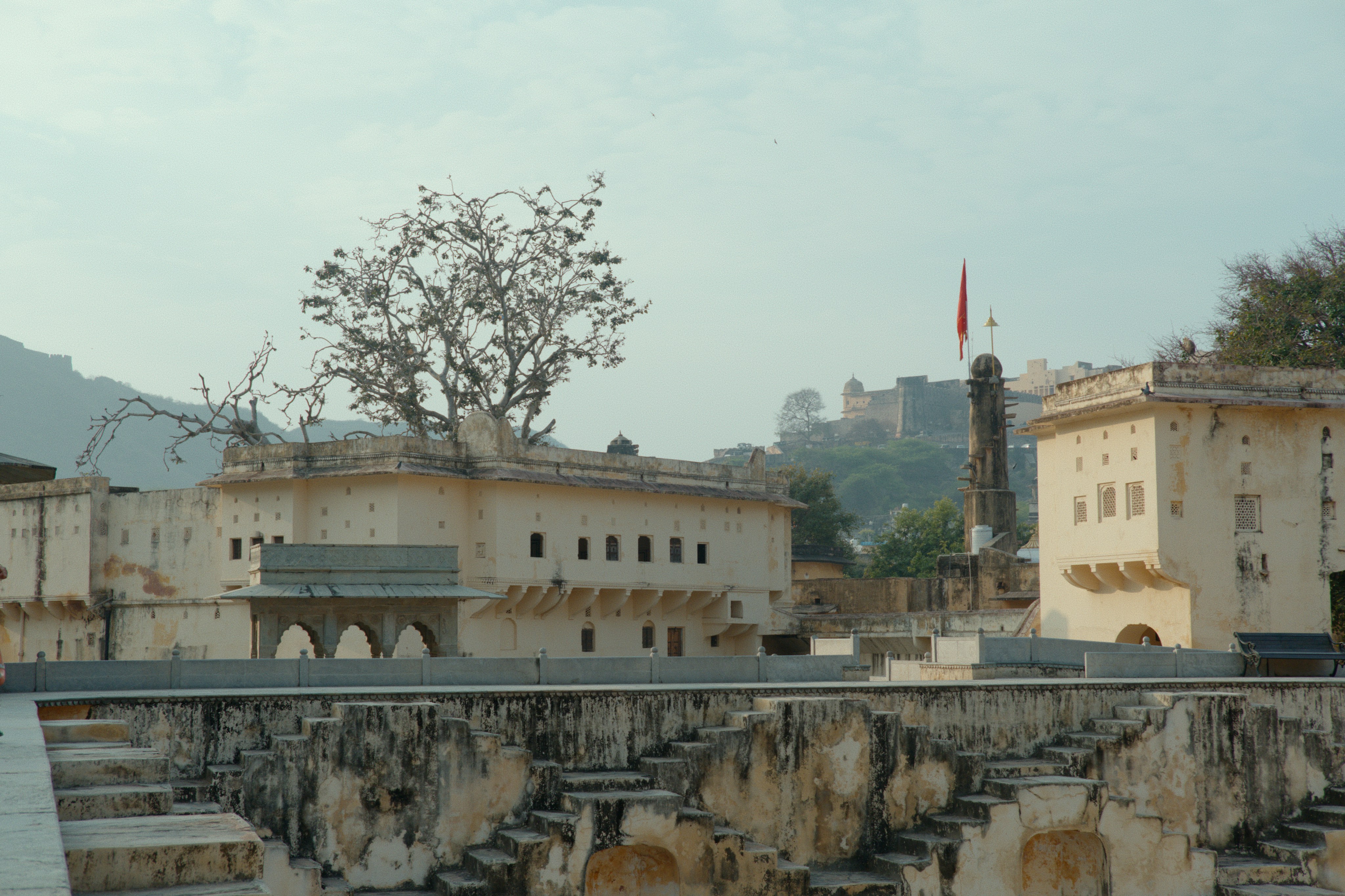 Ancient stepwell with historic buildings and distant hills.