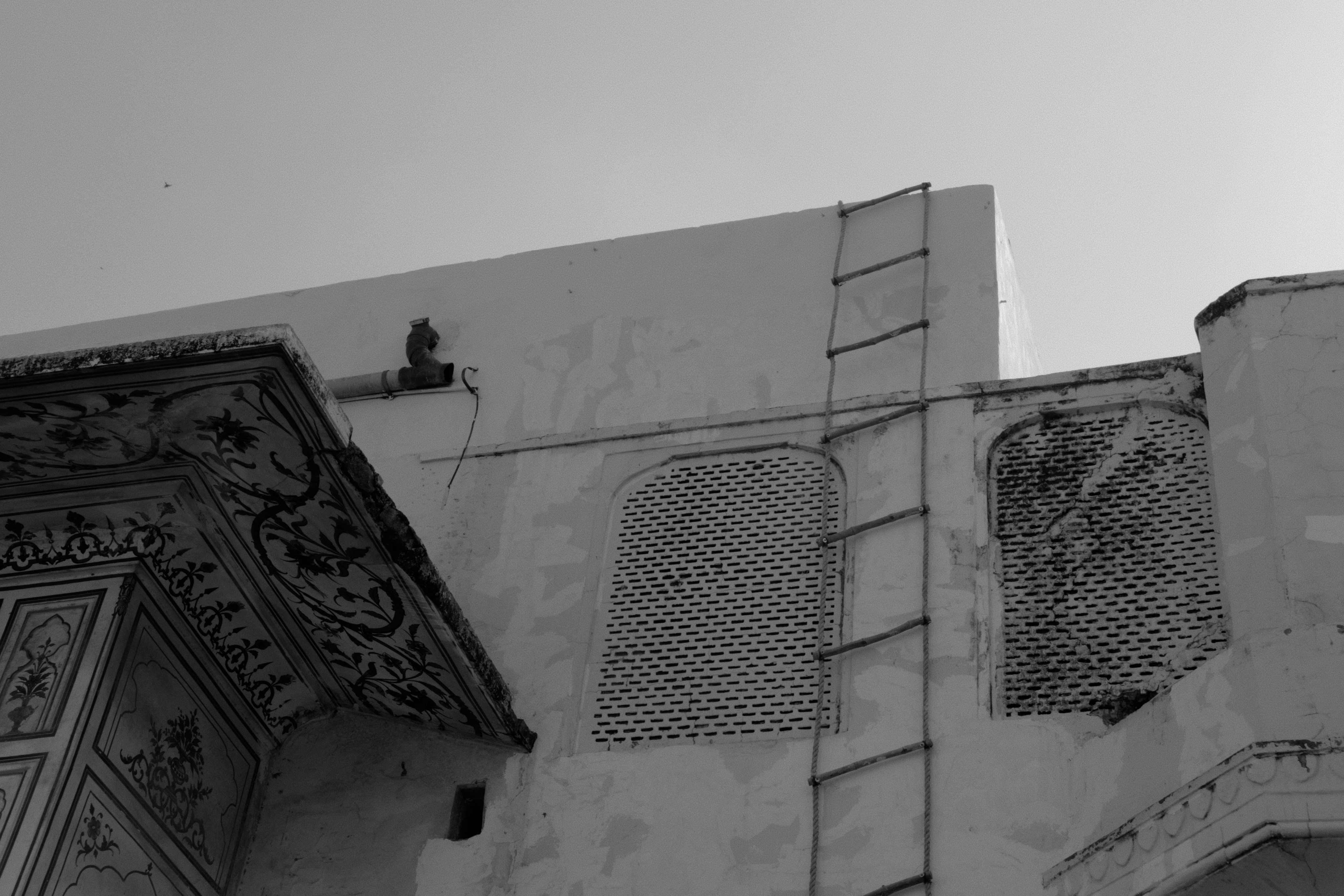 Rusted Ladder and Ornate Corner: Quiet Veranda of a Deteriorating Facade