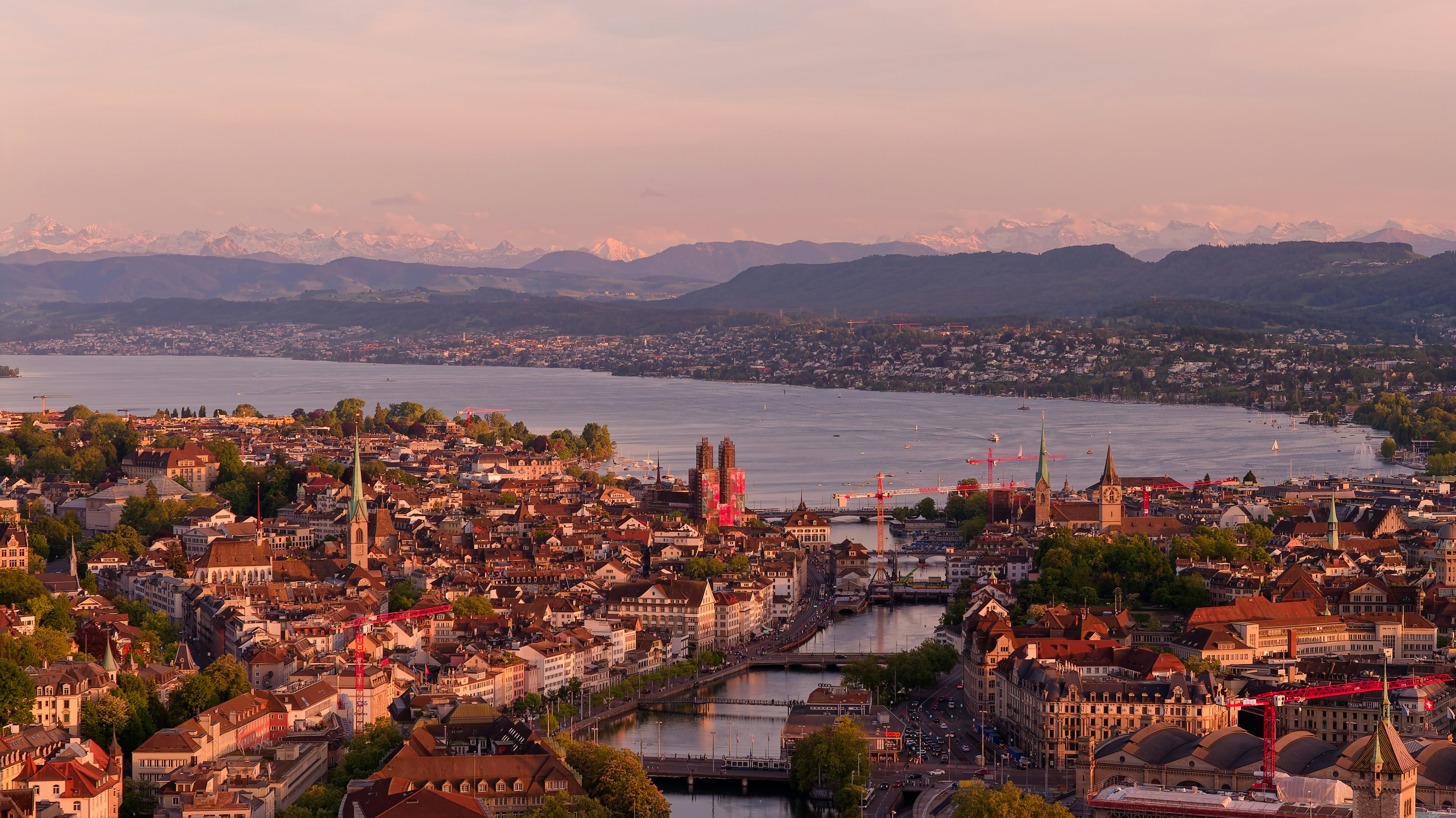 Zurich cityscape with lake, bridges, and distant mountains at sunset.