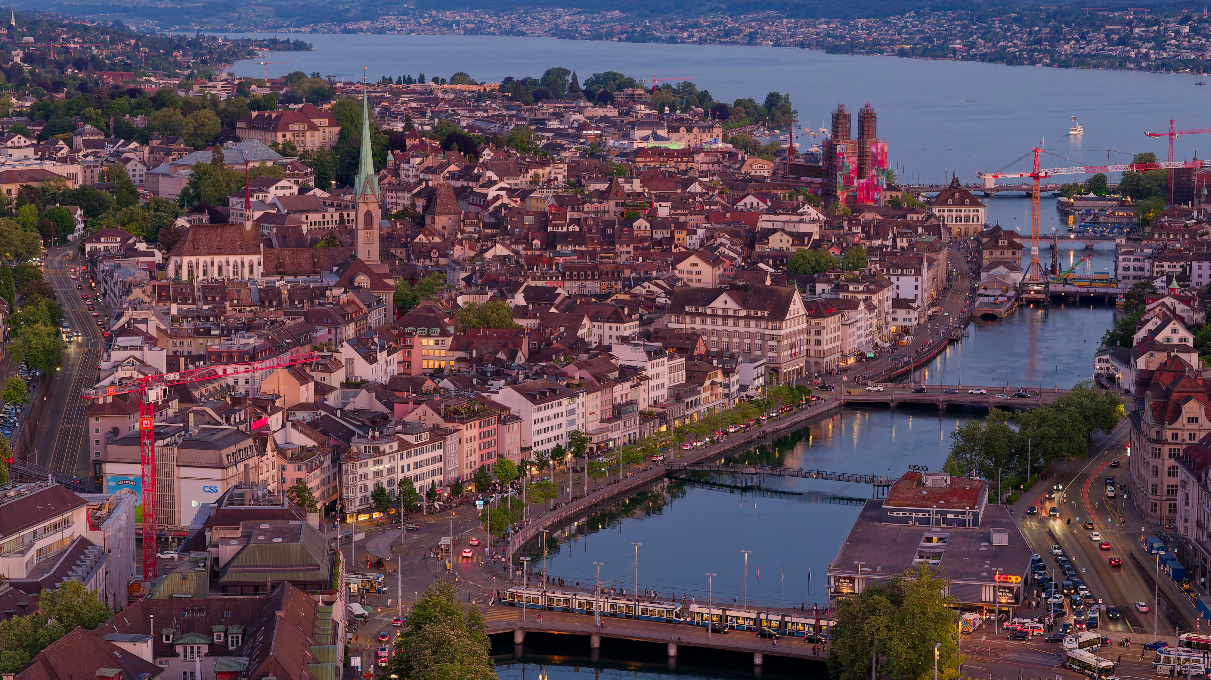Zurich cityscape at dusk with river, buildings, and lake.