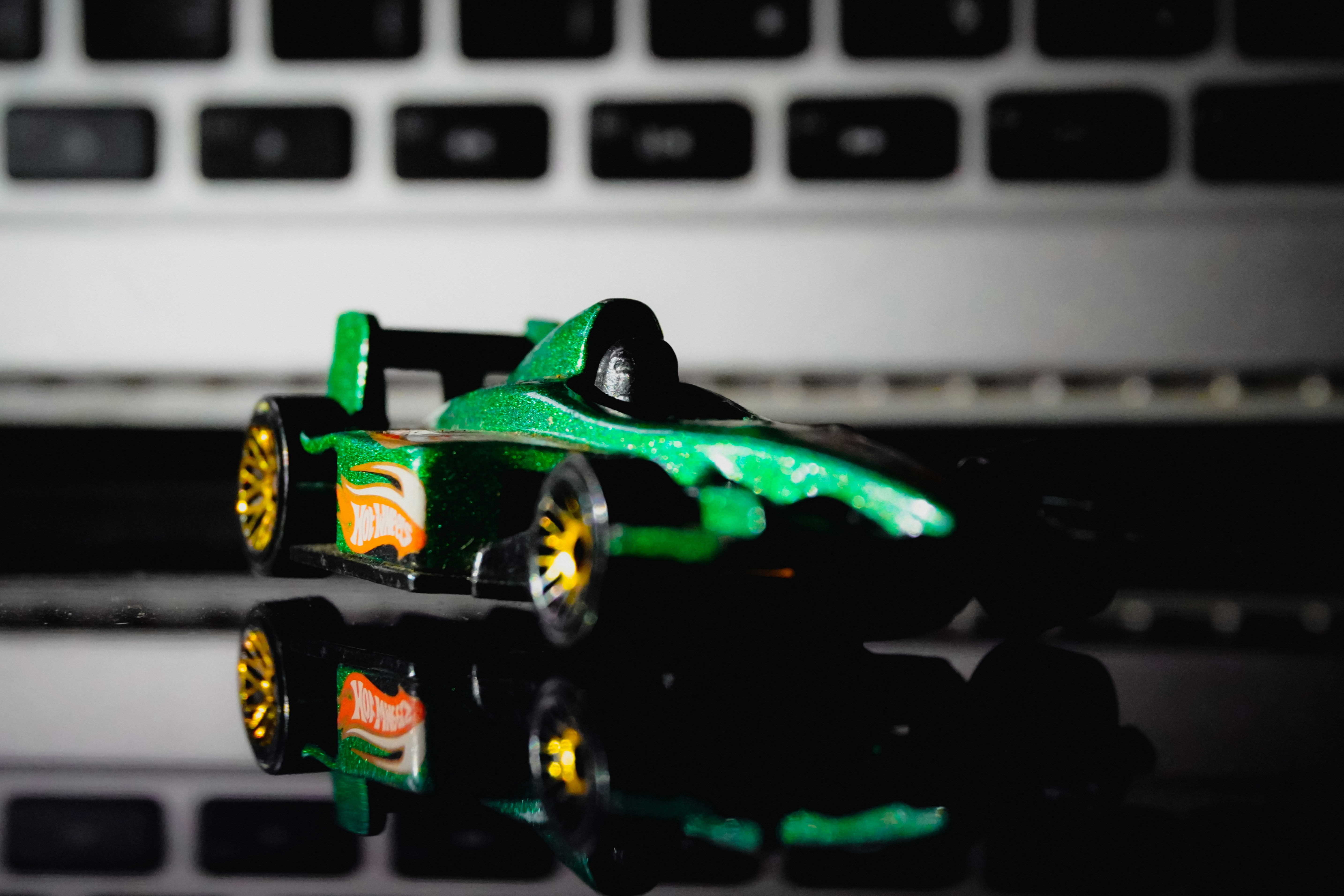Green toy race car resting on a glossy black surface in front of a blurred keyboard
