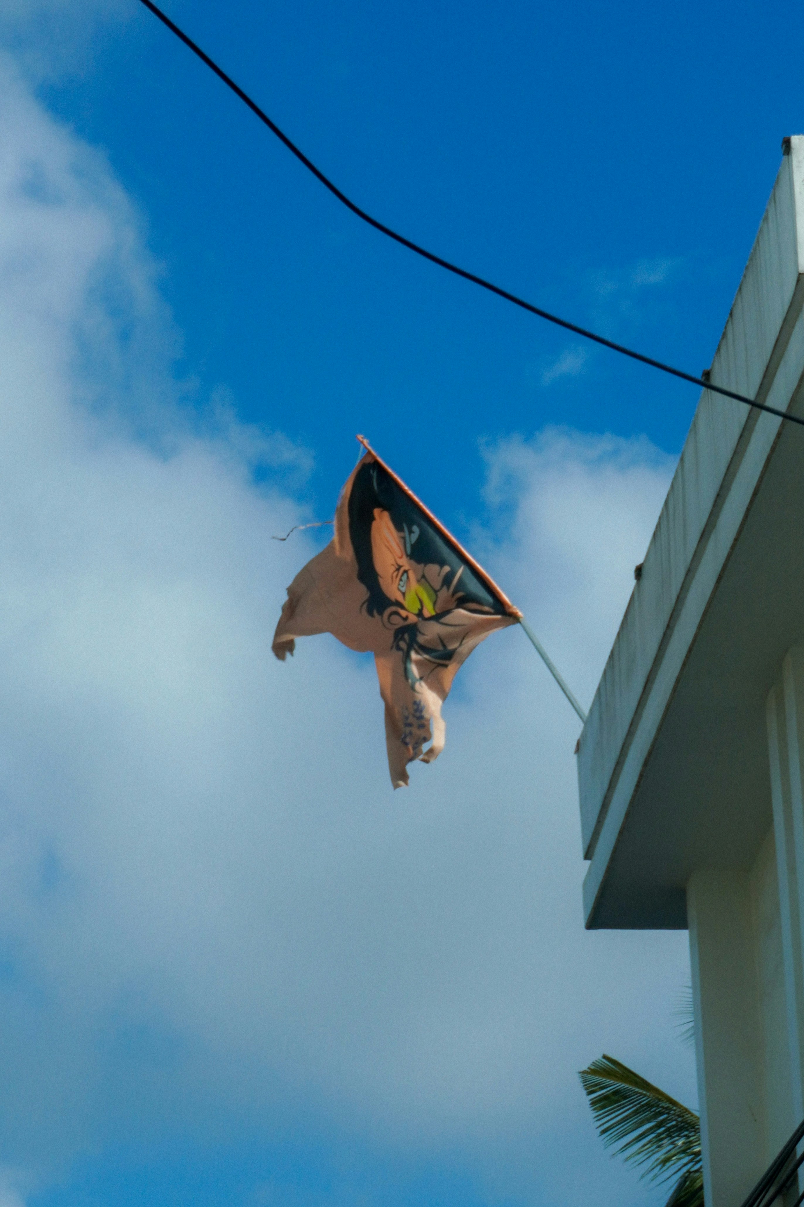Tattered flag flying against a blue sky near a building.
