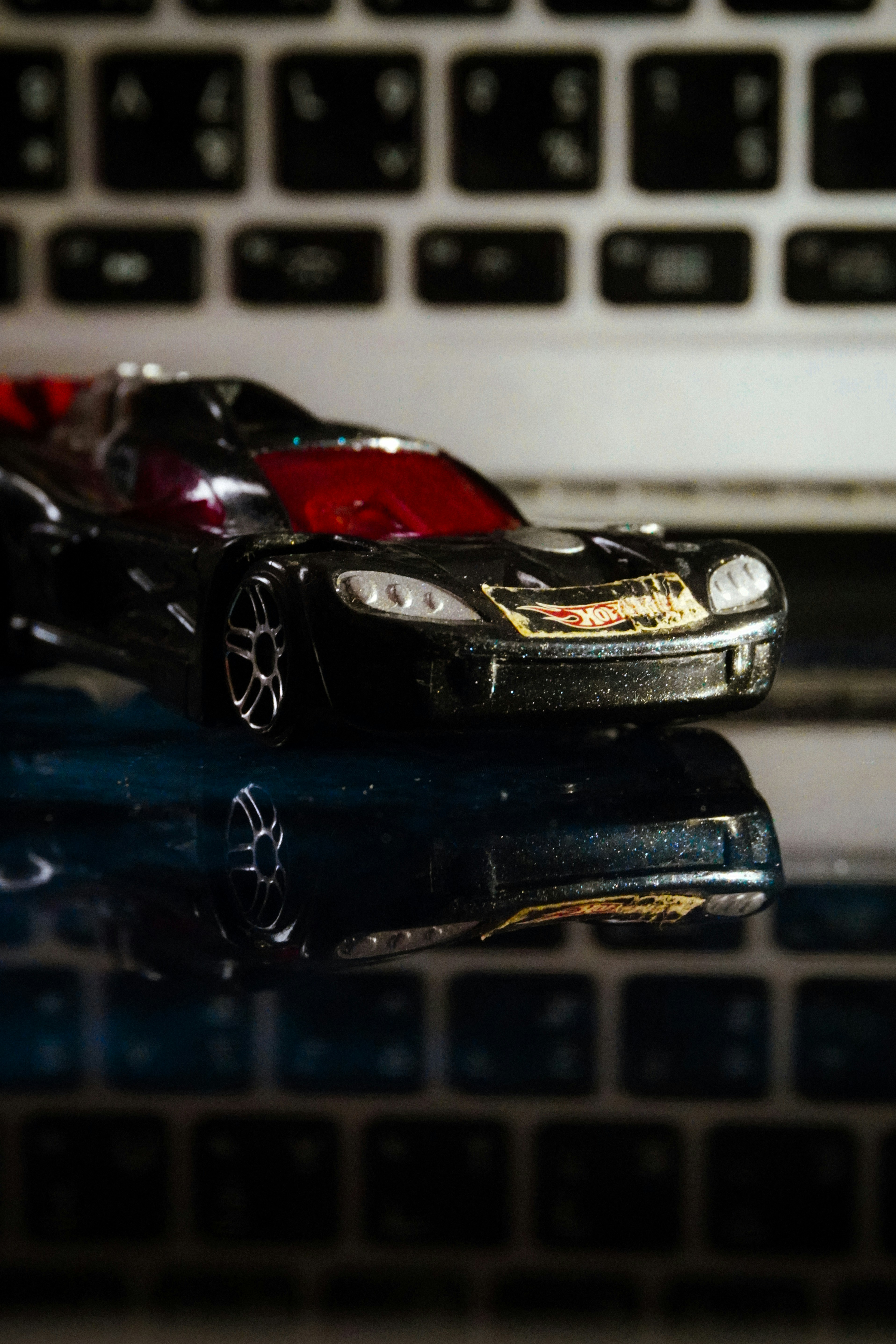 A black hot wheels car on a reflective surface.