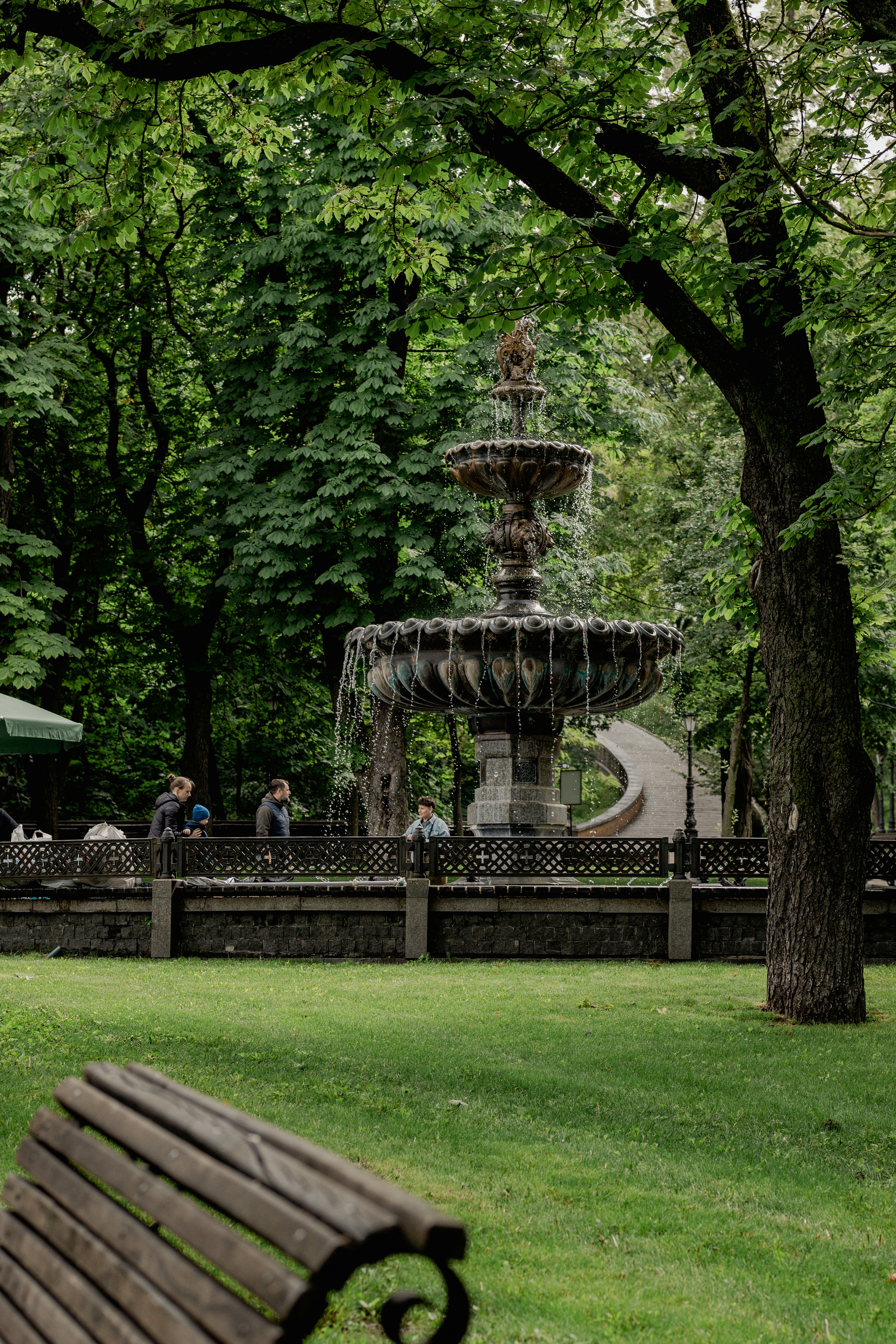 Ornate fountain in a verdant park with a wooden bench.