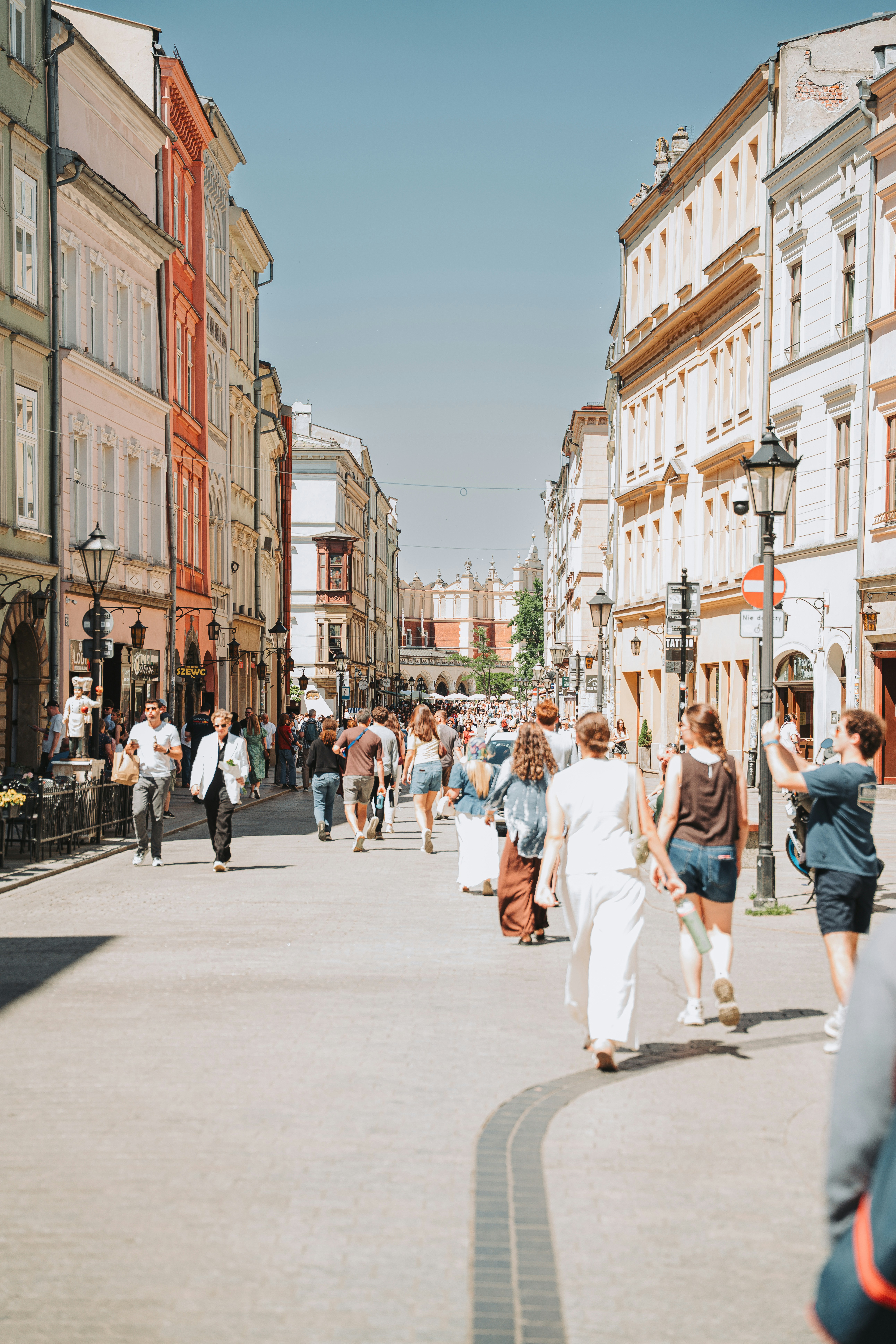 People walk along a sunny street lined with historic buildings.