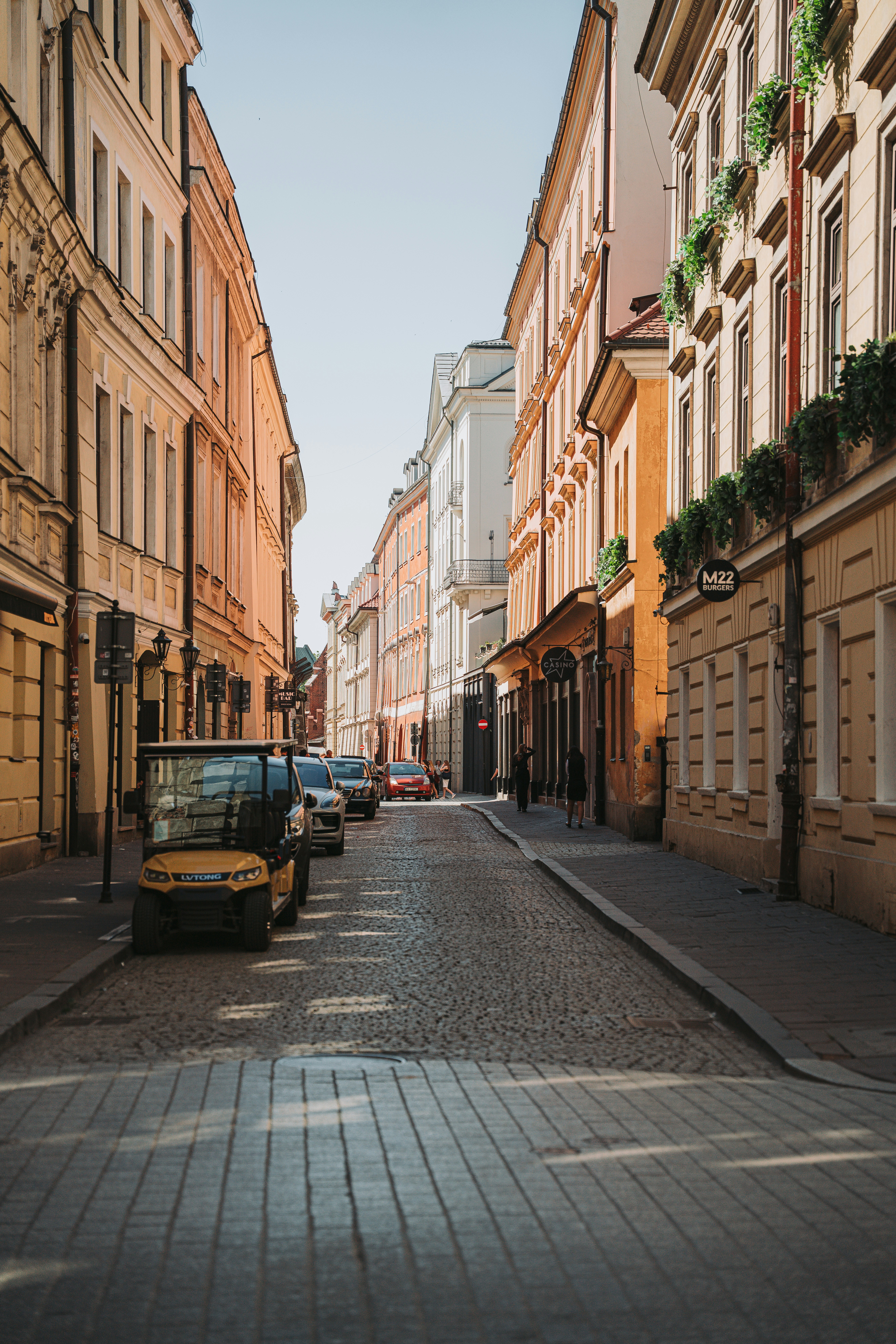 Cobblestone street with old buildings and parked cars.