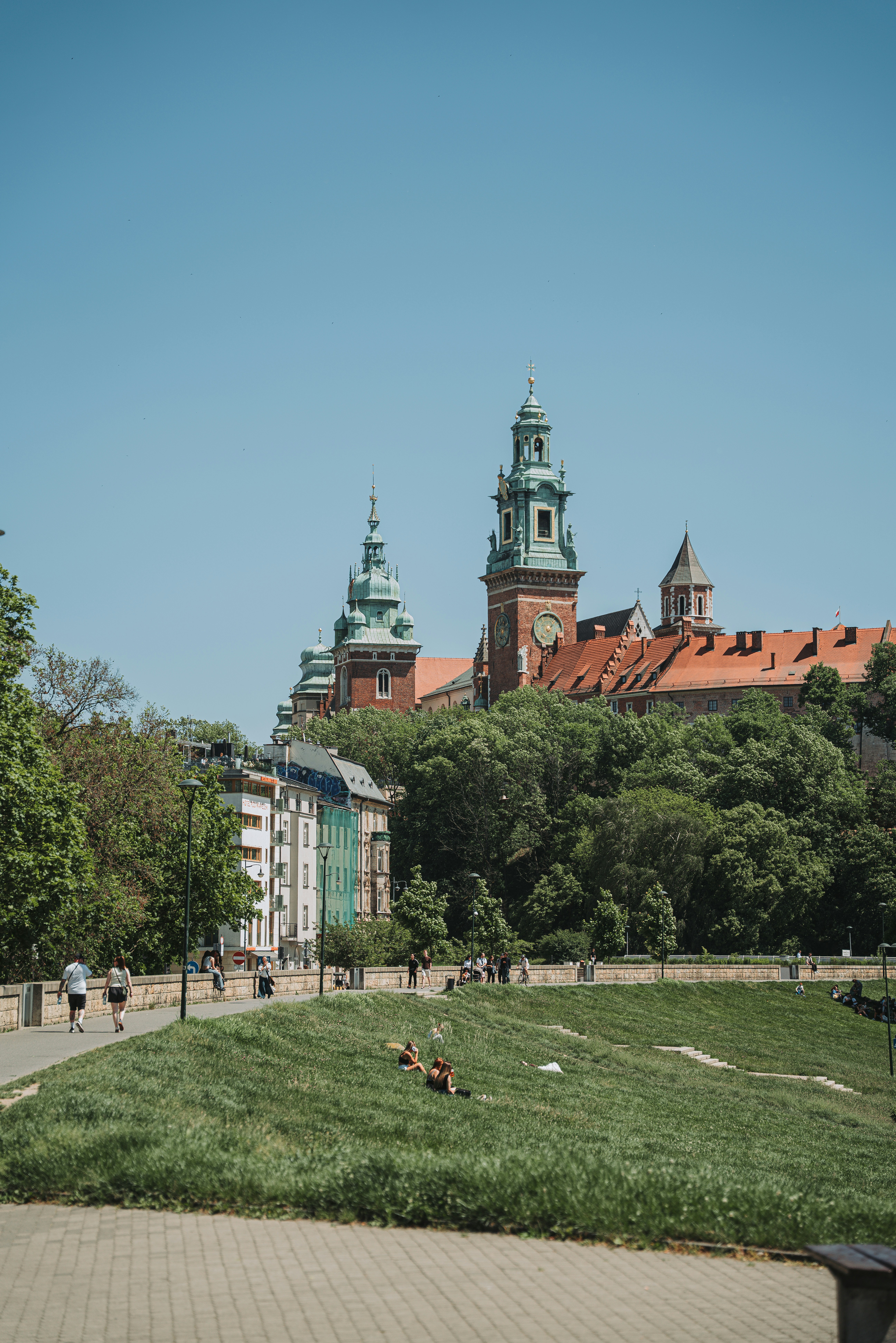 Historic wawel castle overlooks a sunny green park with people.