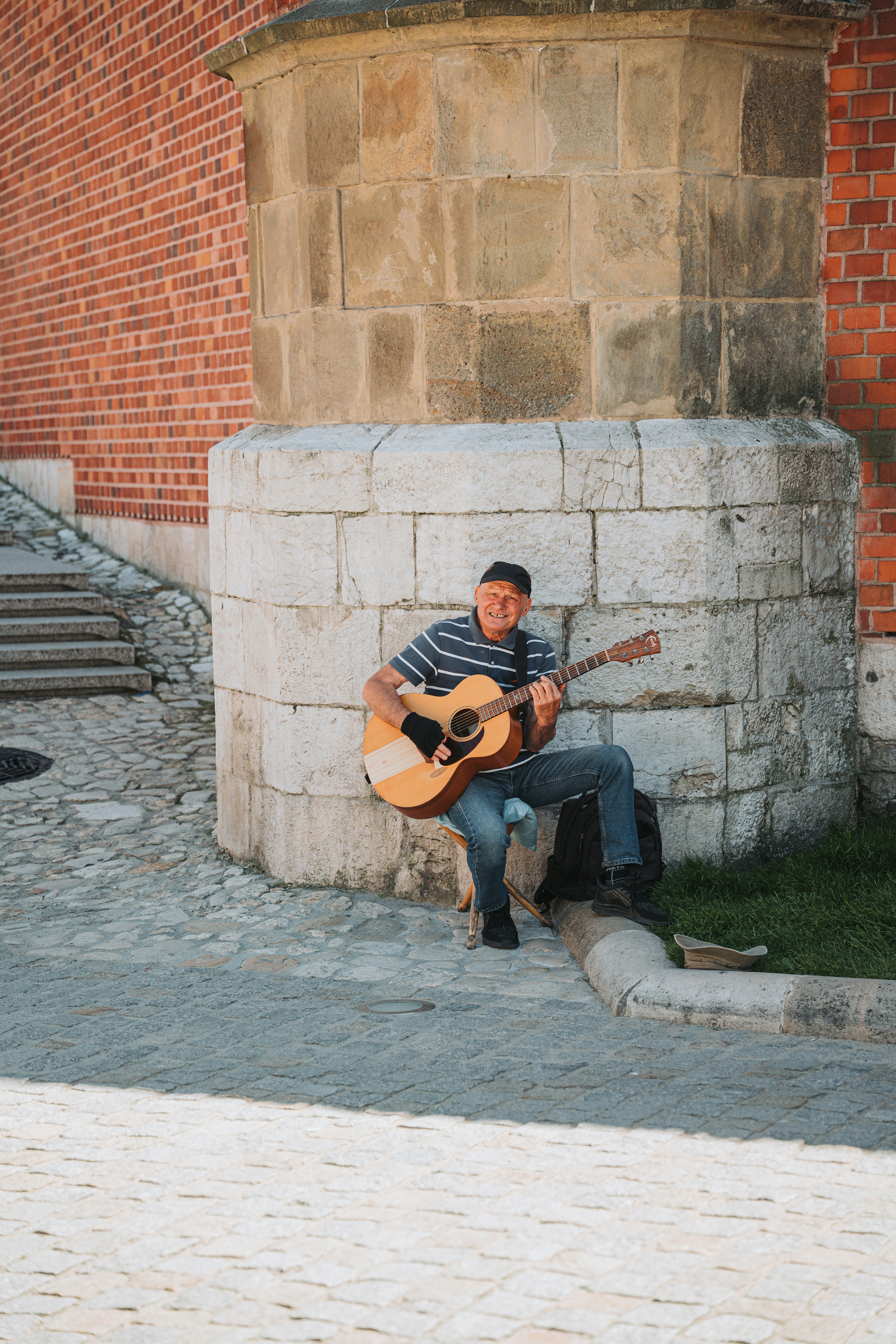 A man plays an acoustic guitar by a stone wall.