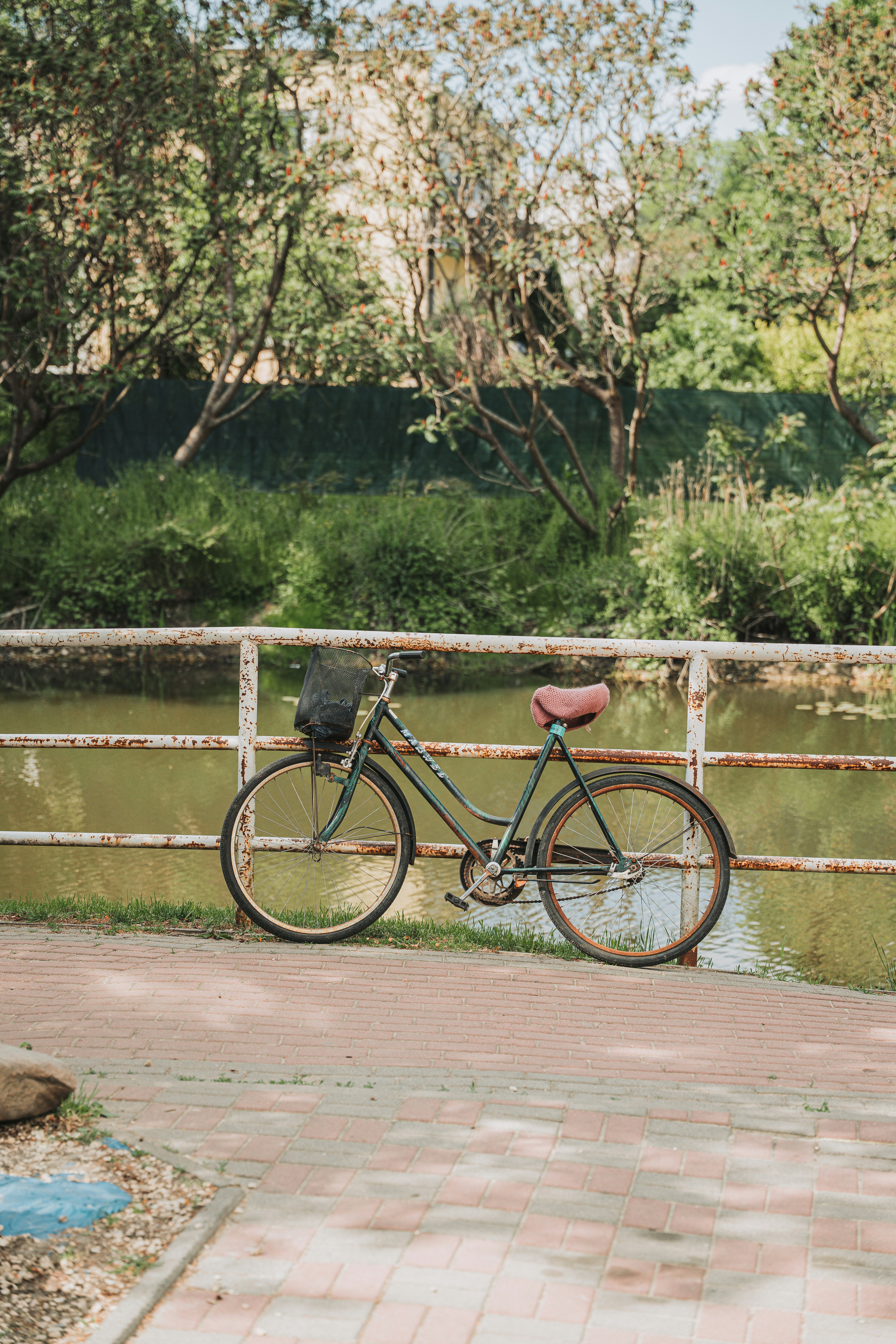 A bicycle leans against a rusty railing by a river.