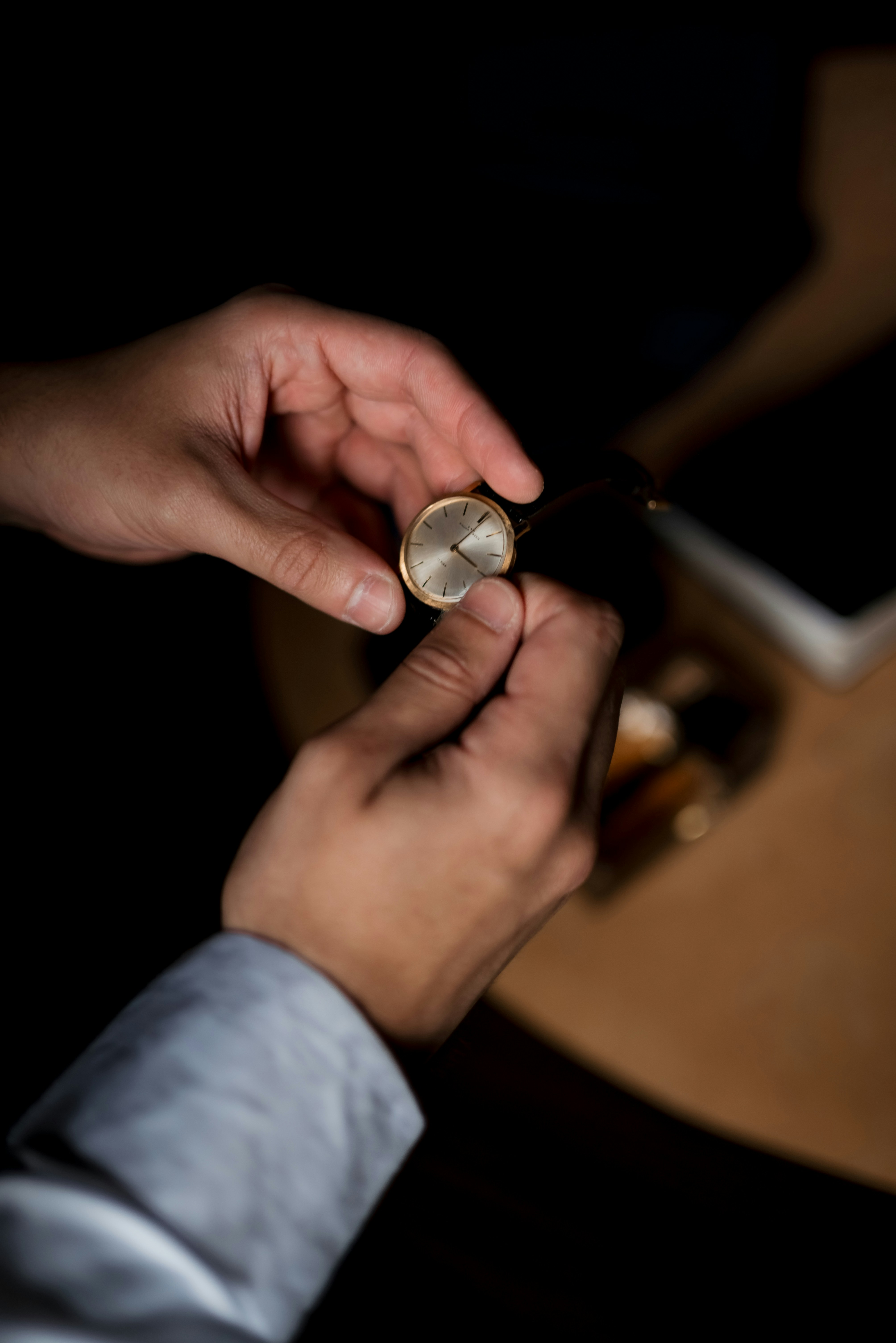 Ticking Moment: Hands Adjust a Gold-Toned Wristwatch in Low Light