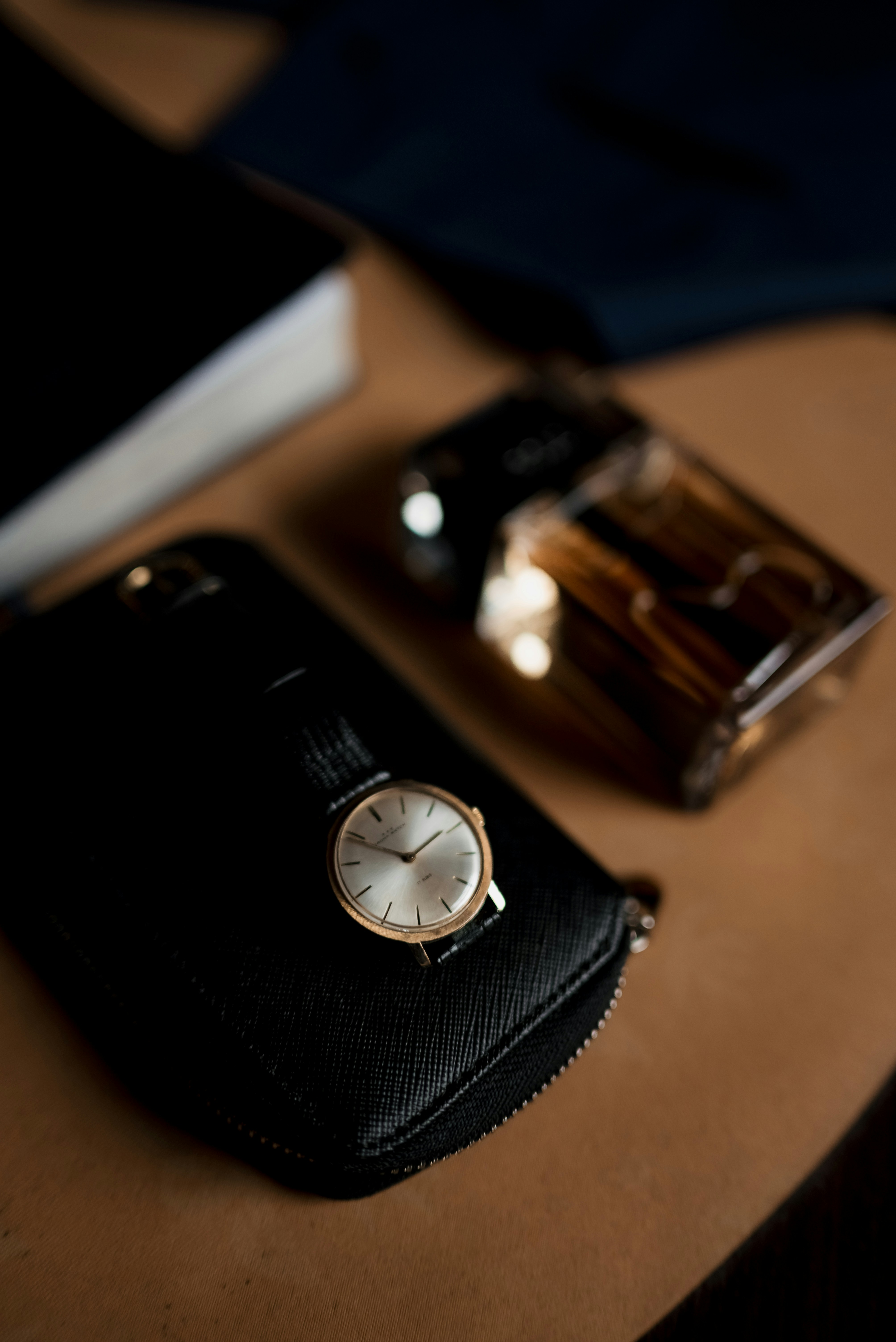 Elegant watch on black wallet, with perfume and book.