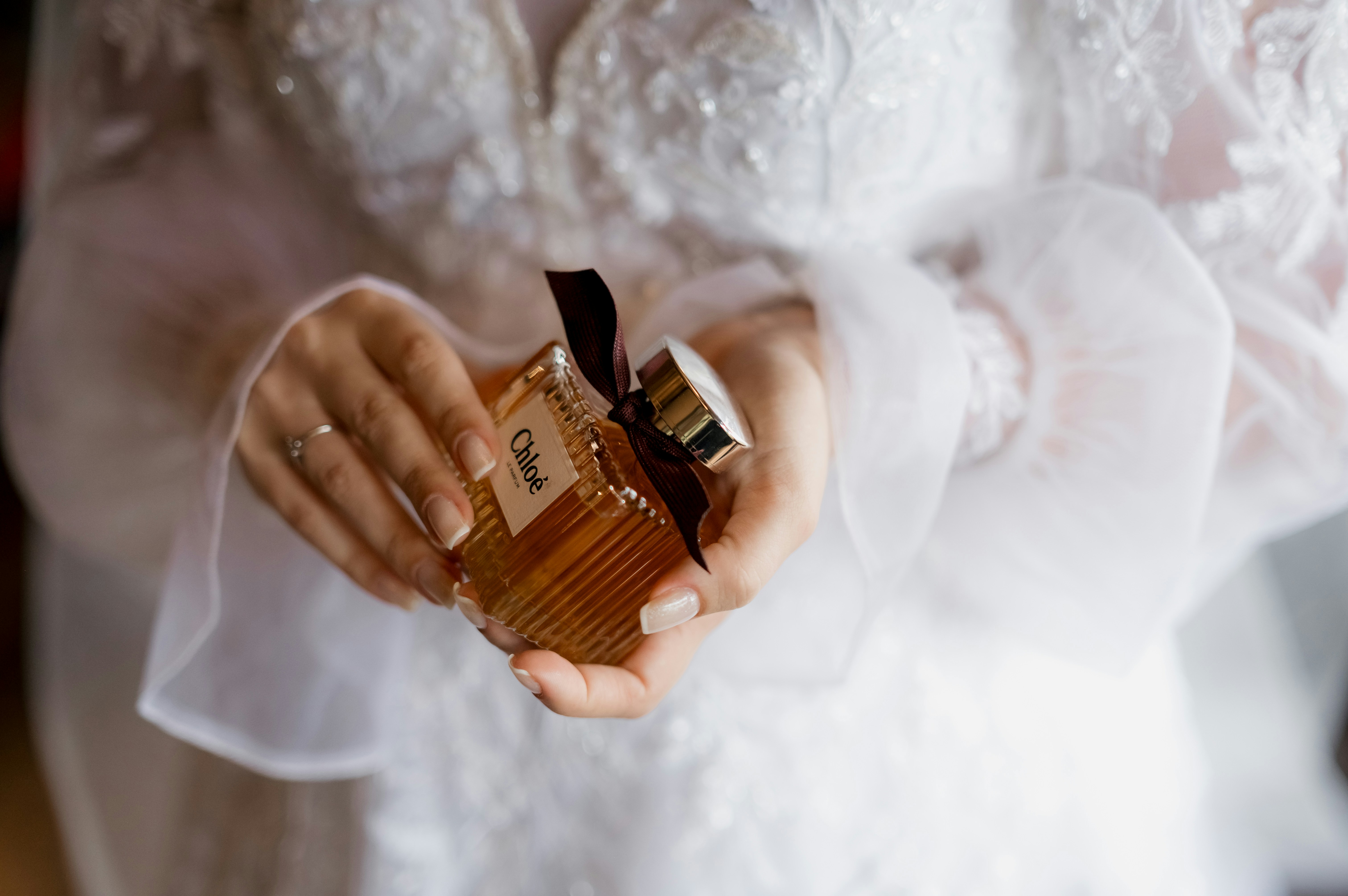 A bride in a white dress holds a perfume bottle.