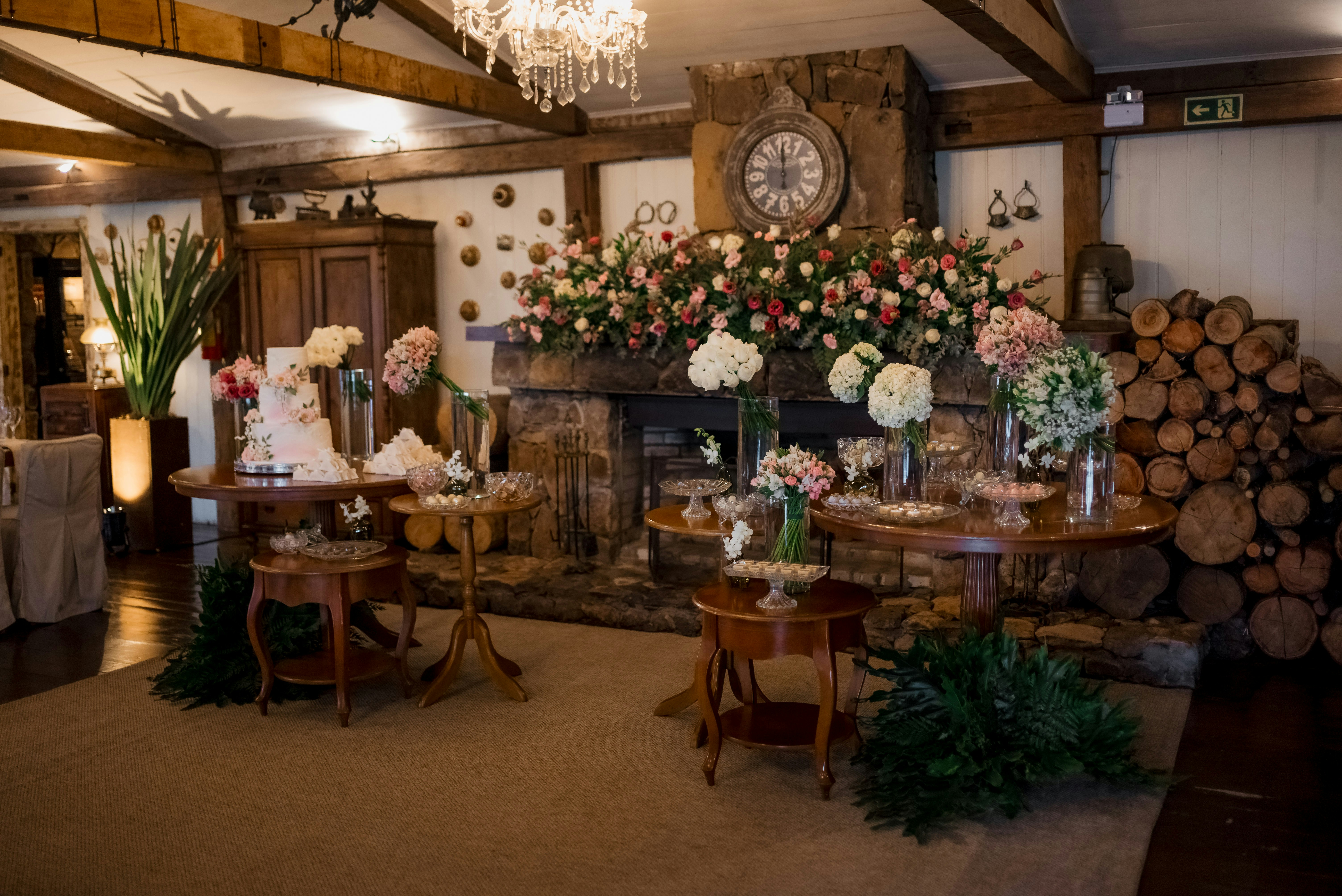 Elegant rustic room with fireplace, flowers, cakes, and stacked firewood.