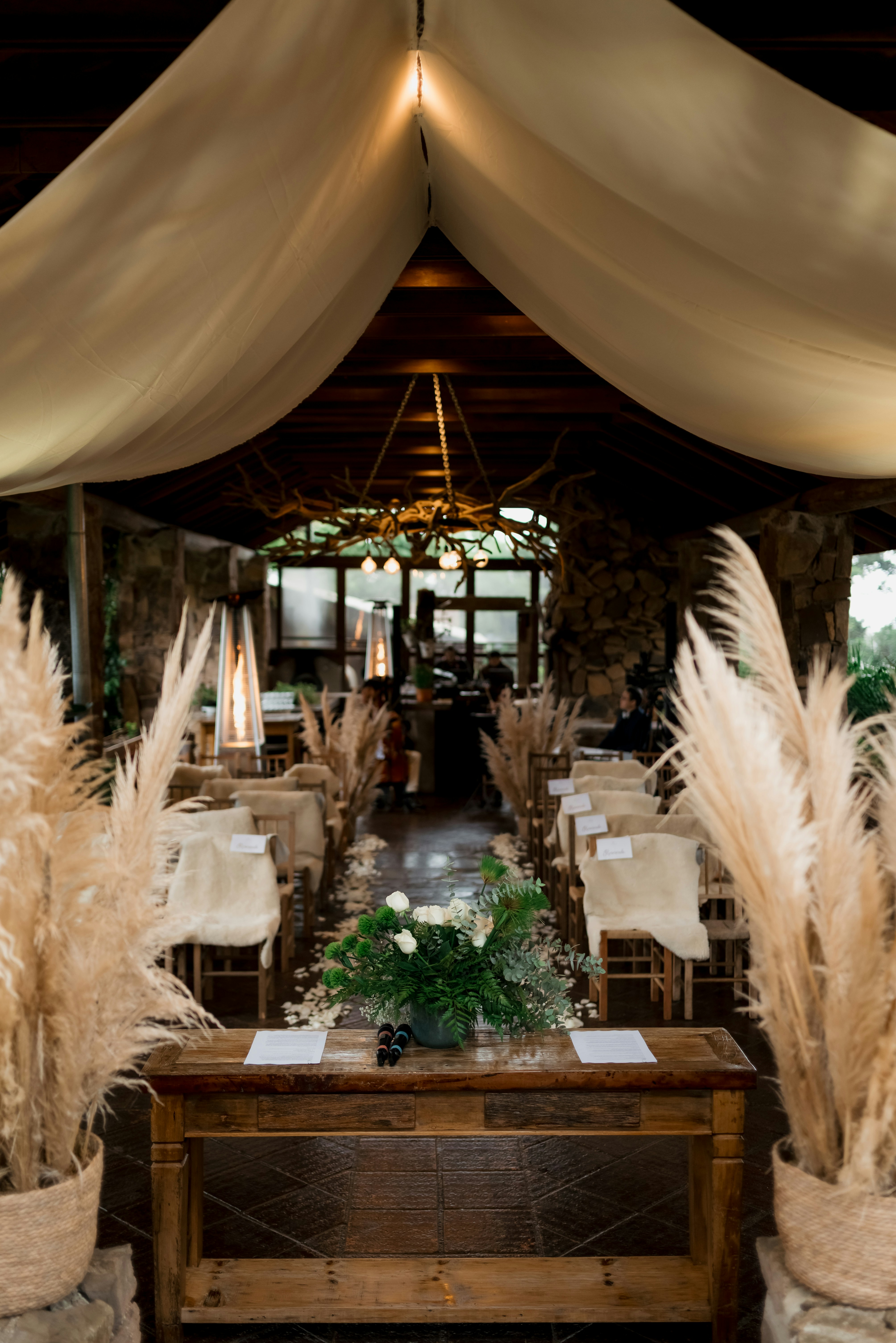 Rustic wedding ceremony setup with pampas grass and draped ceiling.