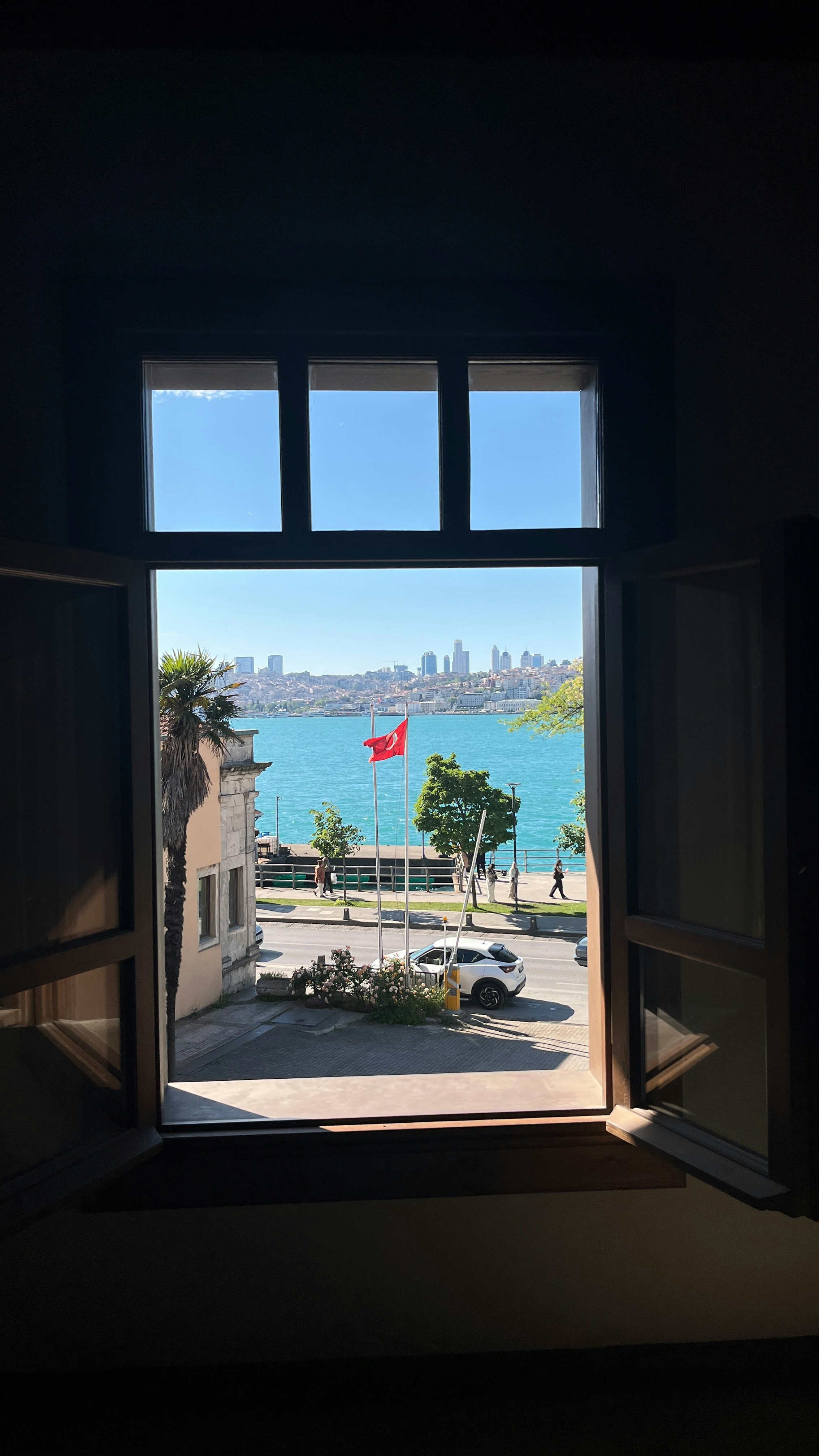 A View Through the Window: Waterfront Skyline and Flag by the Shore
