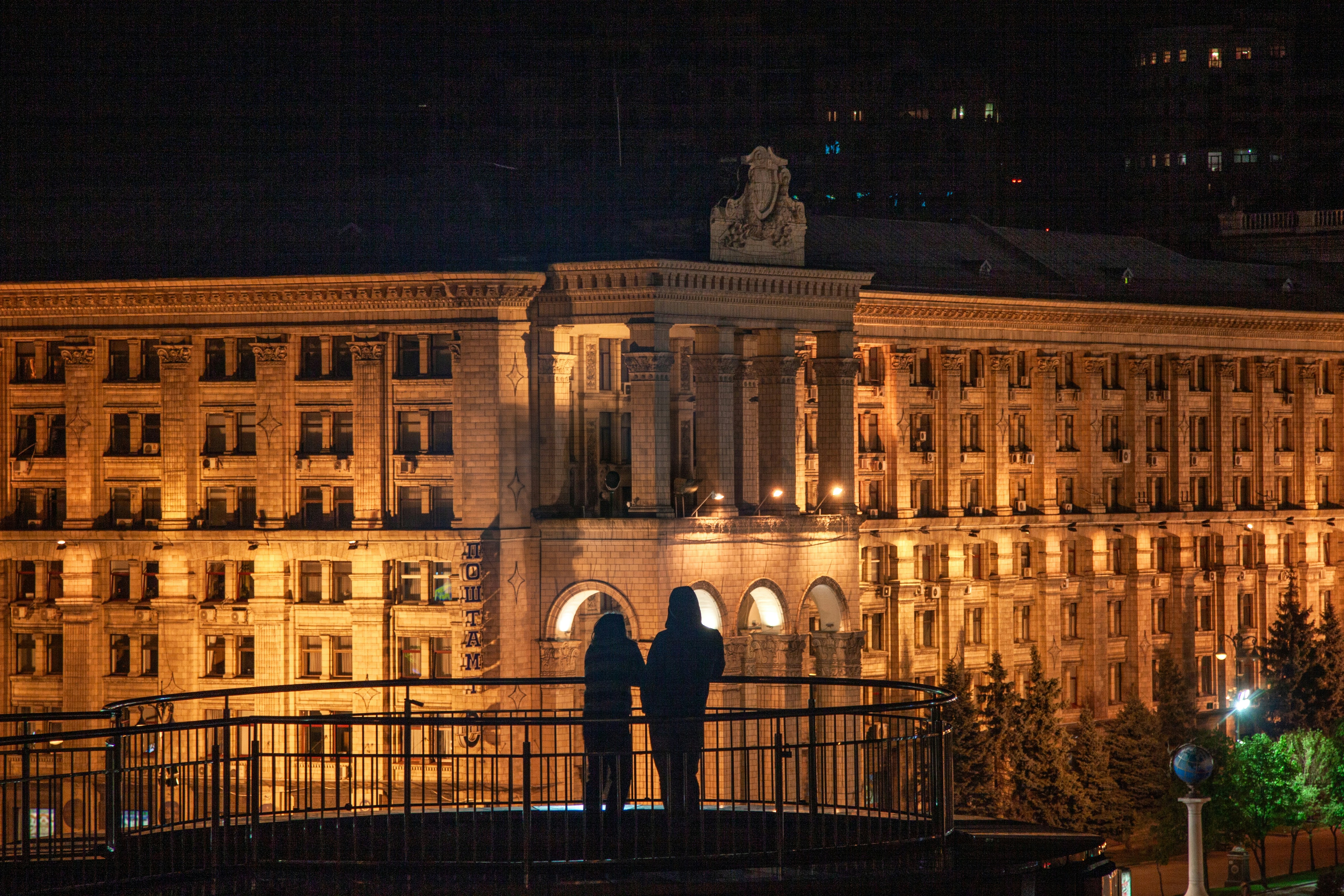 Night Couple on the Arch Bridge: silhouettes Against a City’s Warm Facade