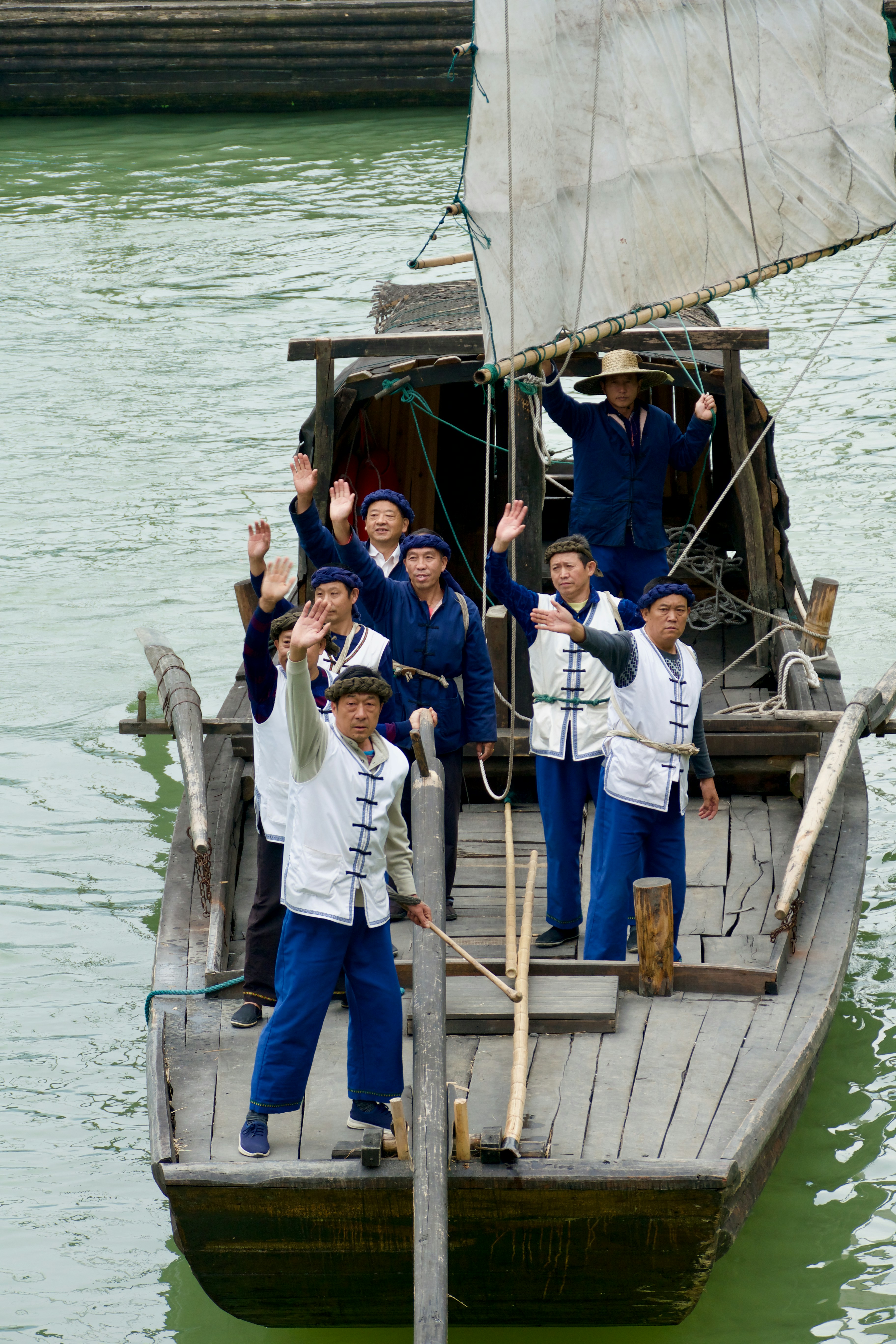 People in traditional clothes waving from a wooden boat.