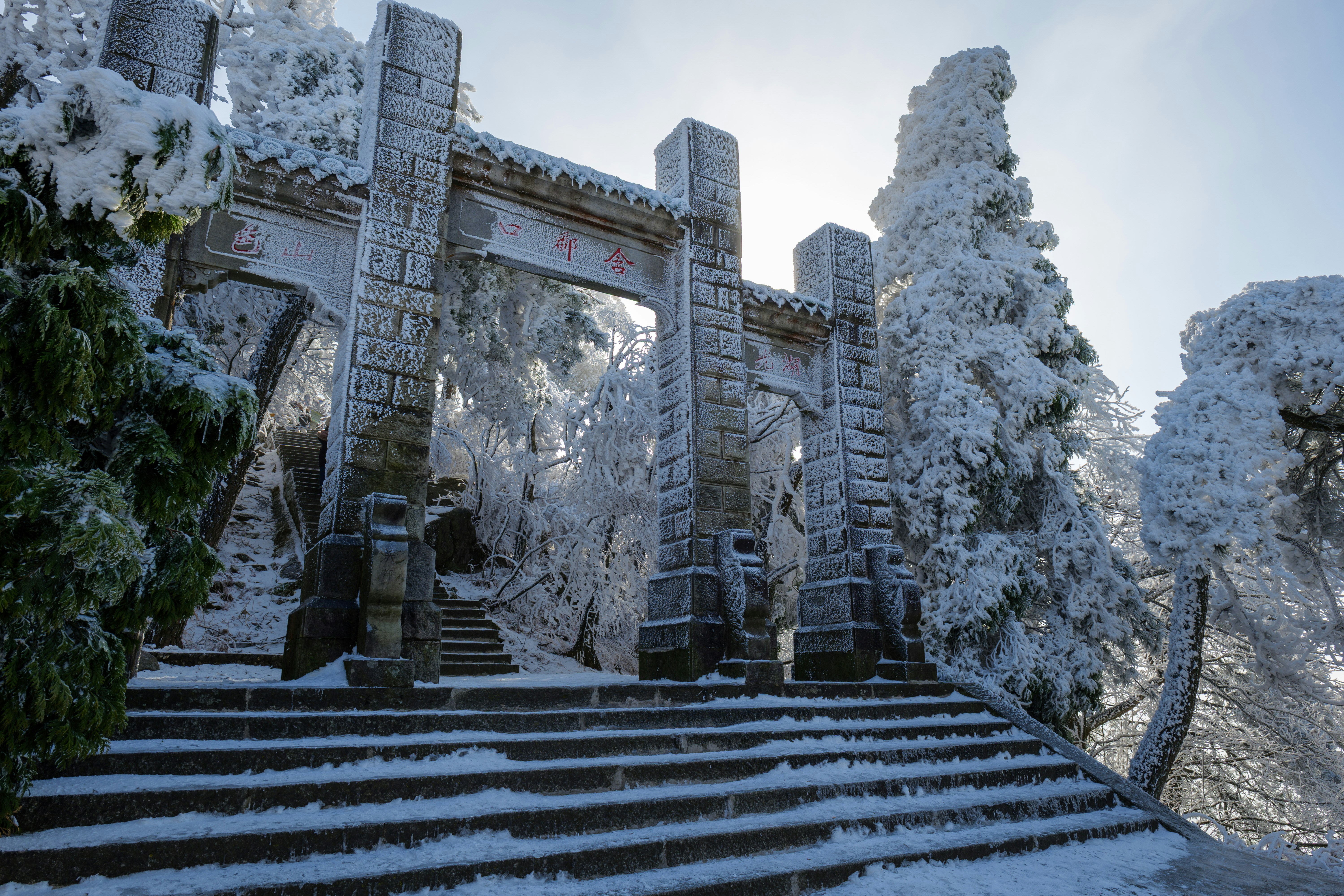 Snowy stone archway with steps and frost-covered trees.