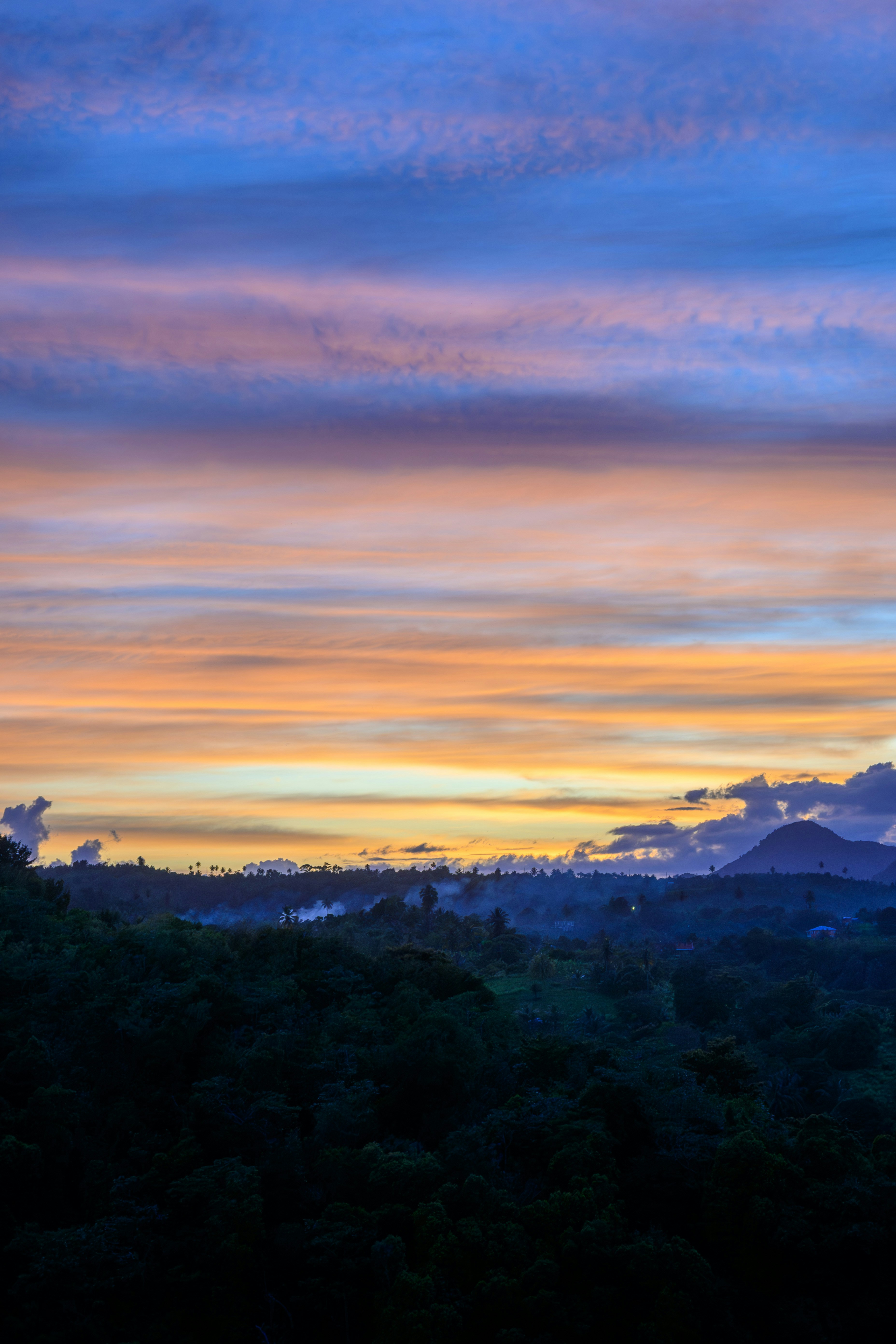 A vibrant sunset sky over dark hills and trees.