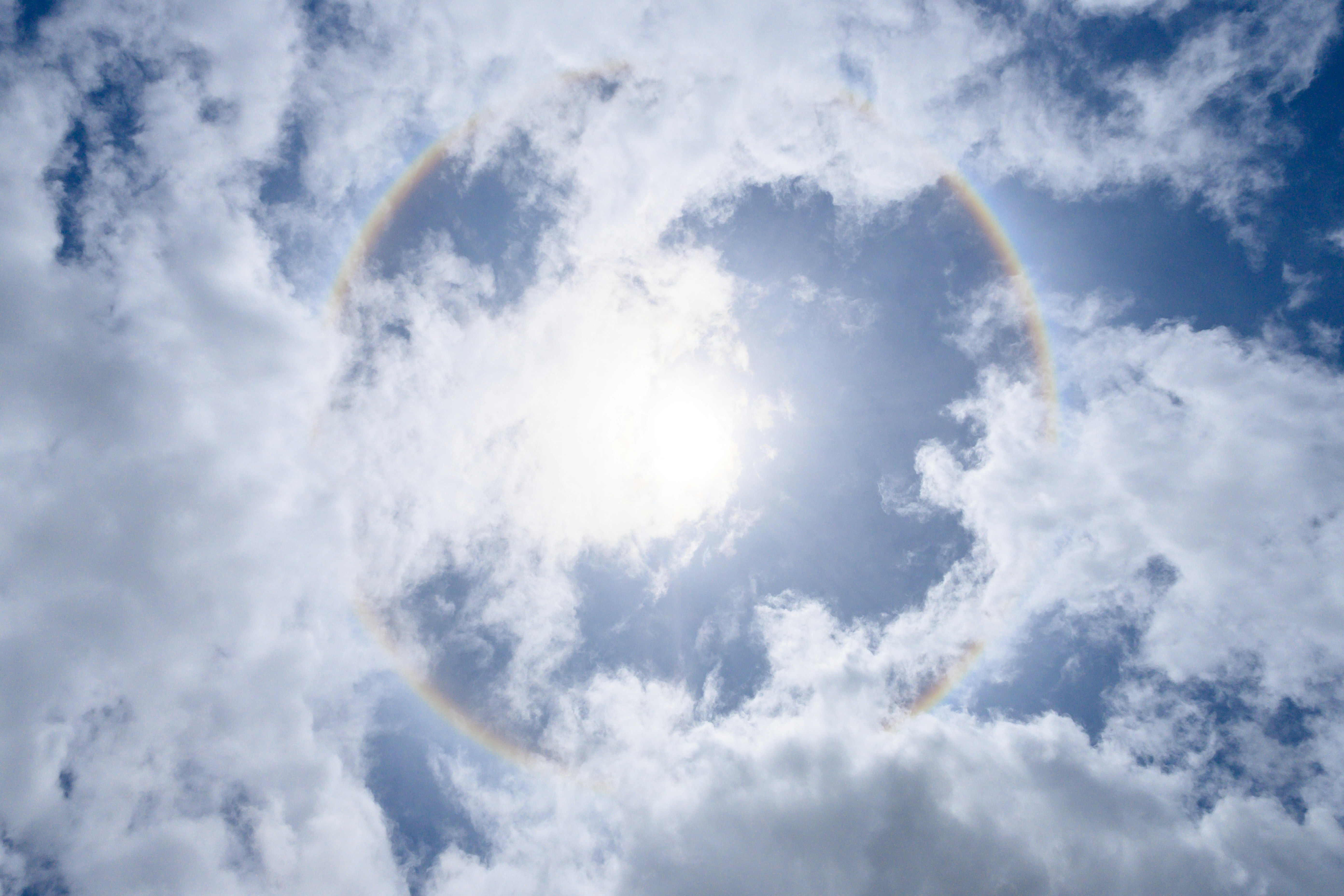 Bright sun with a circular halo surrounded by white clouds.