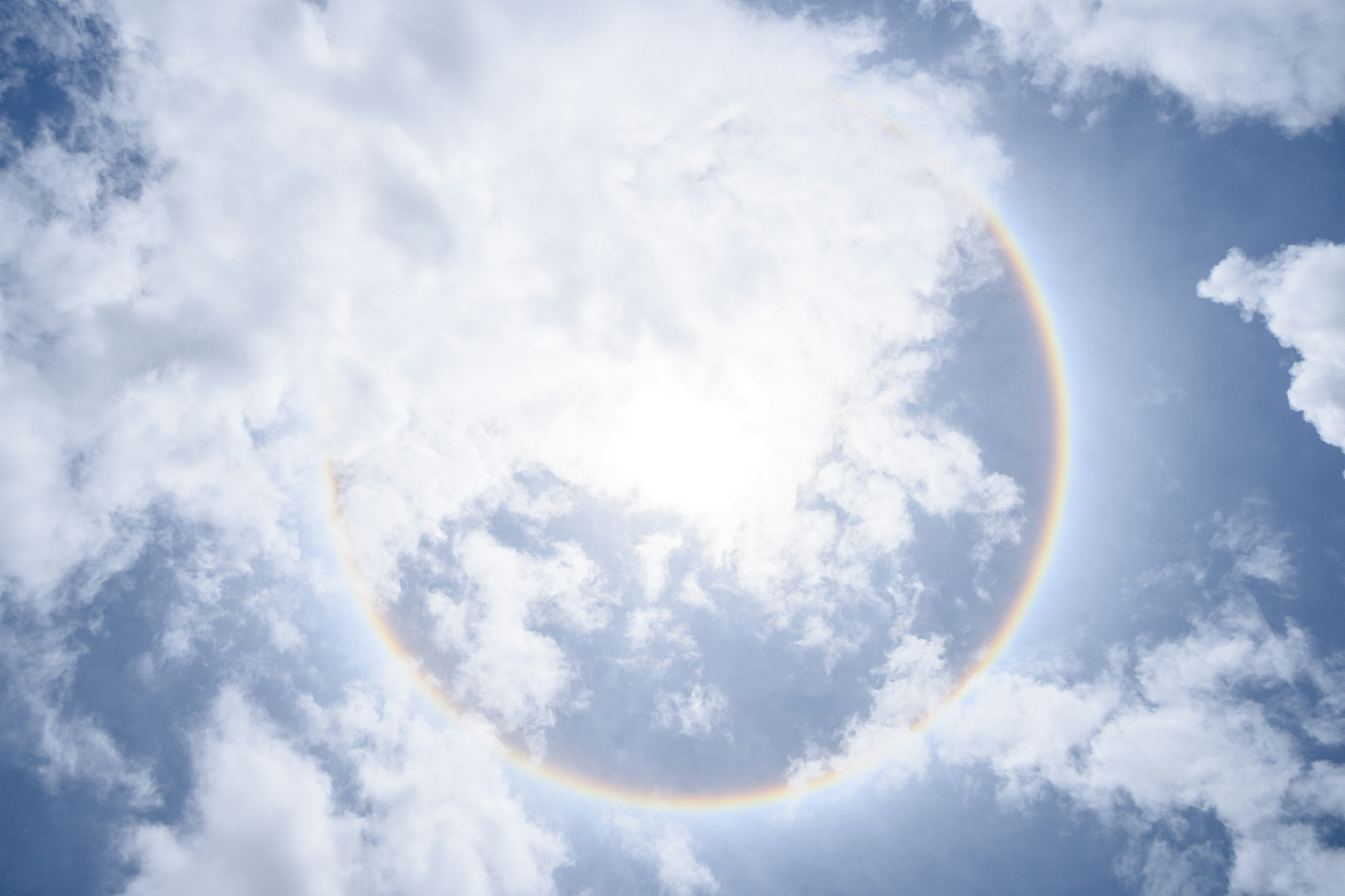 A sun halo visible through clouds in a blue sky.