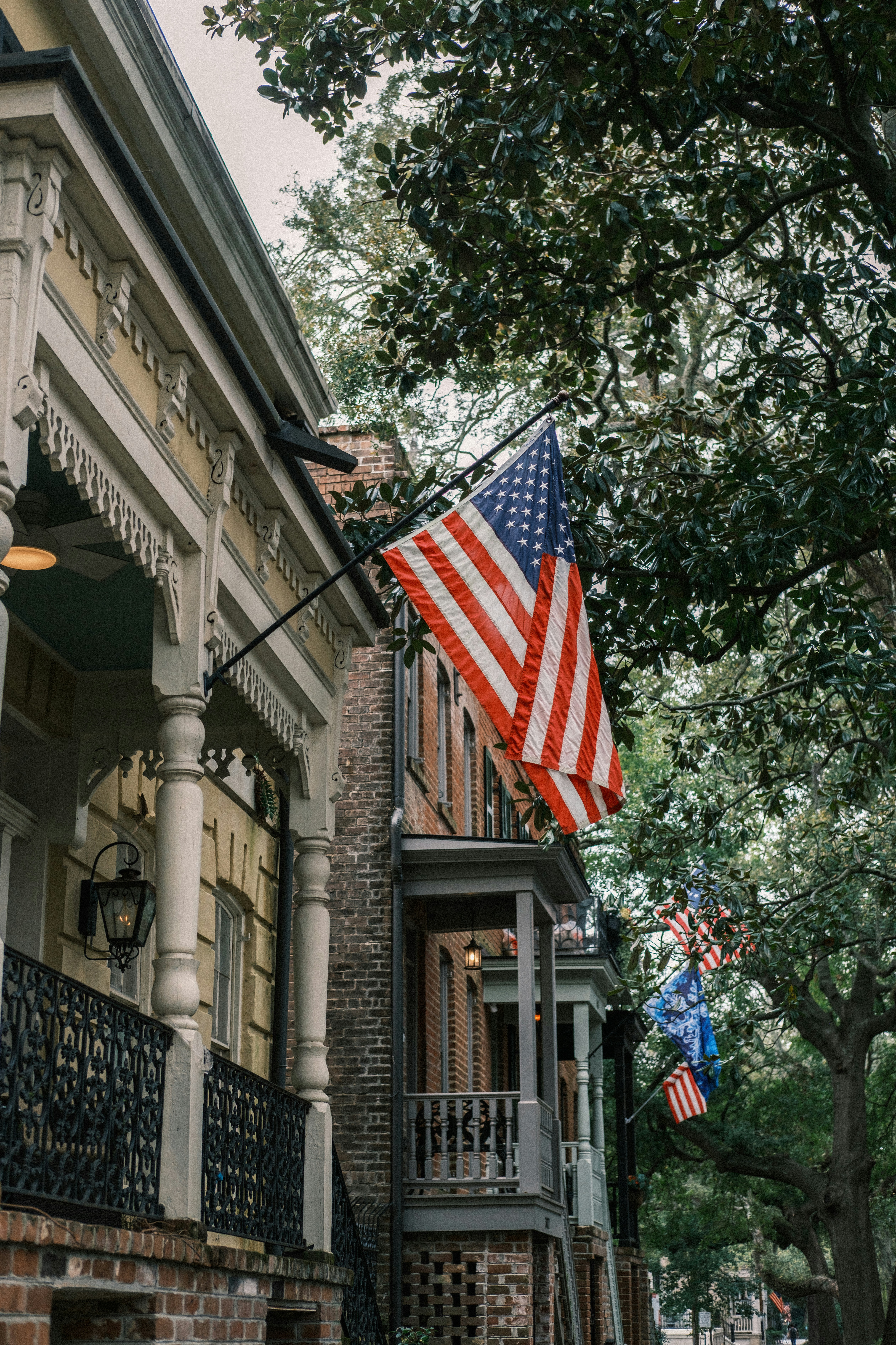American flags hang from historic buildings on a tree-lined street.