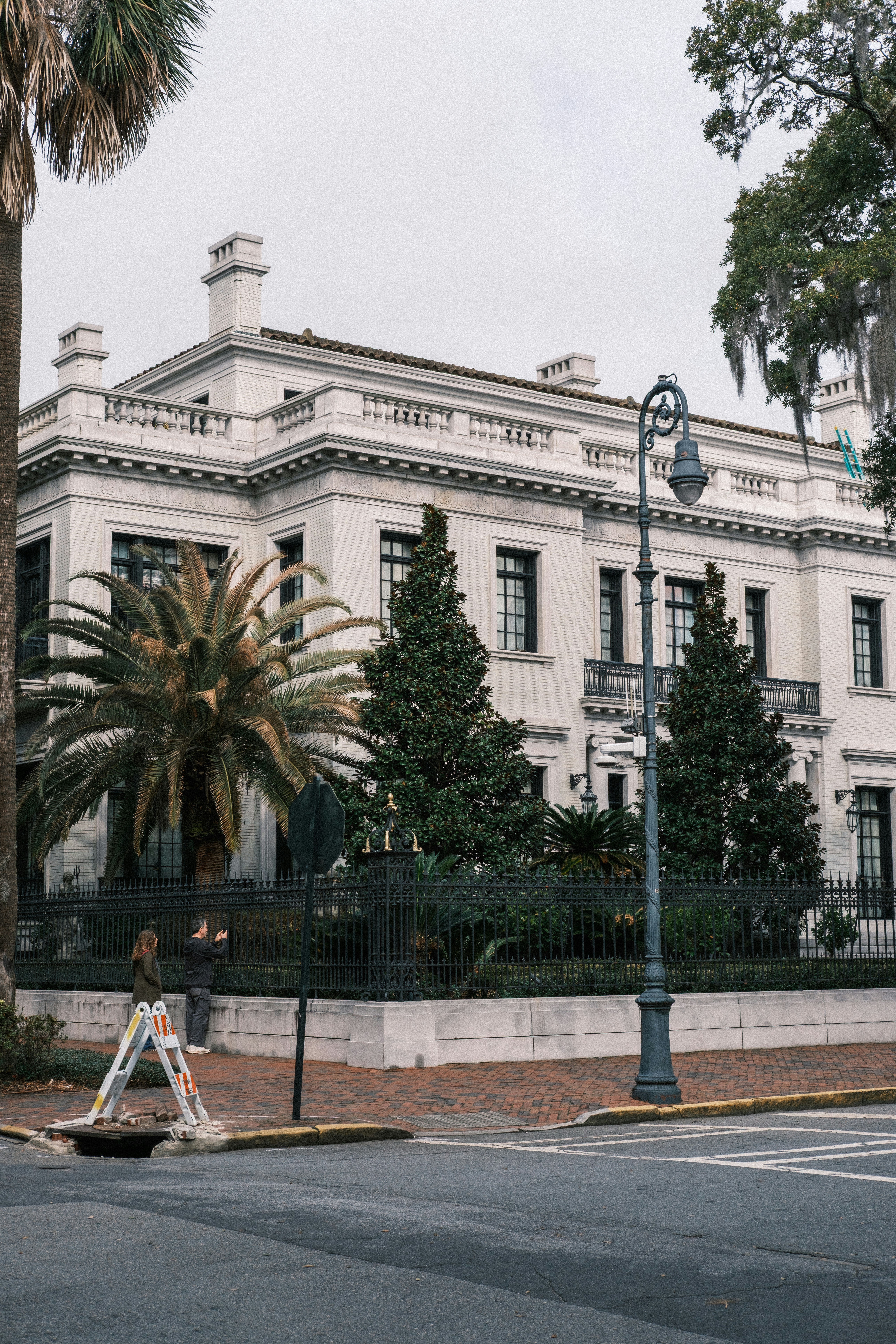 Ornate white mansion with palm trees and a street.