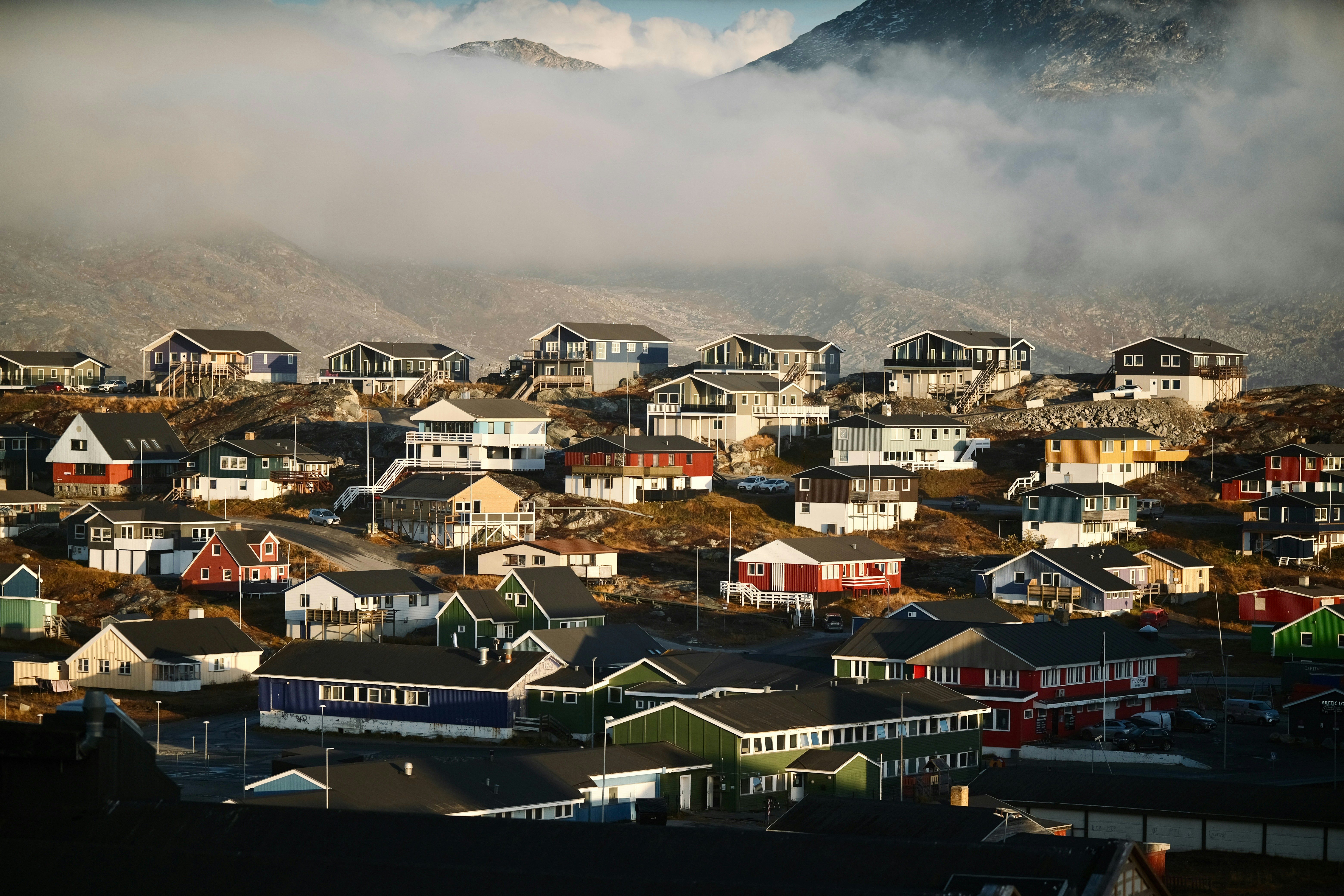Colorful cottages cling to a sunlit hillside under a veil of low clouds