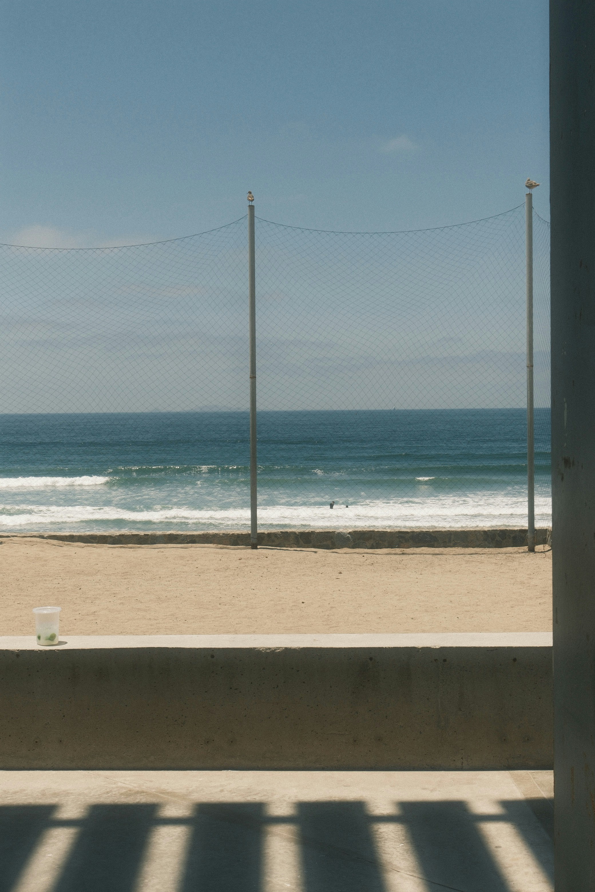 Sandy beach, ocean waves, and poles under a blue sky.