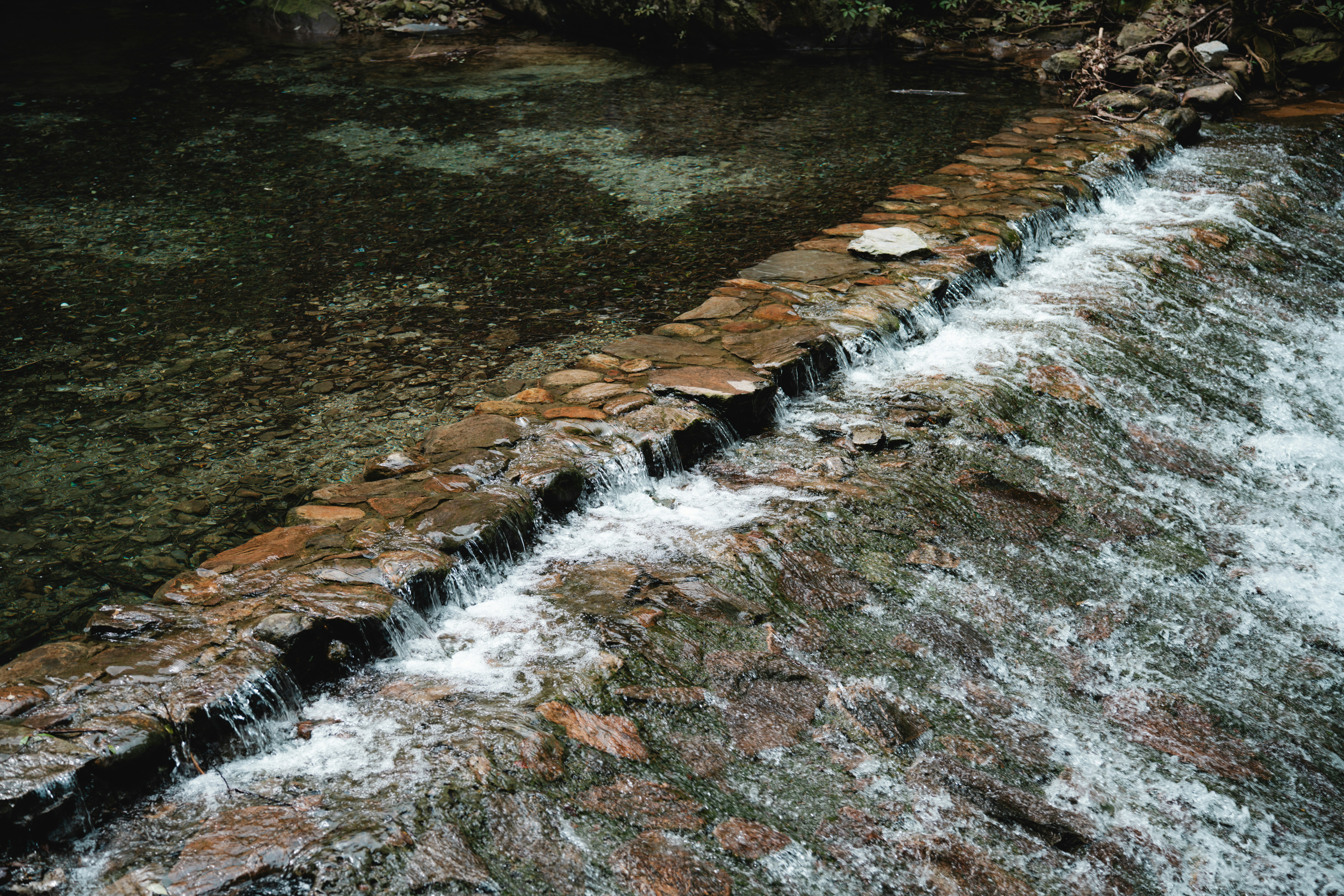 Stone-rimmed Shallow Cascade Across a Quiet Stream