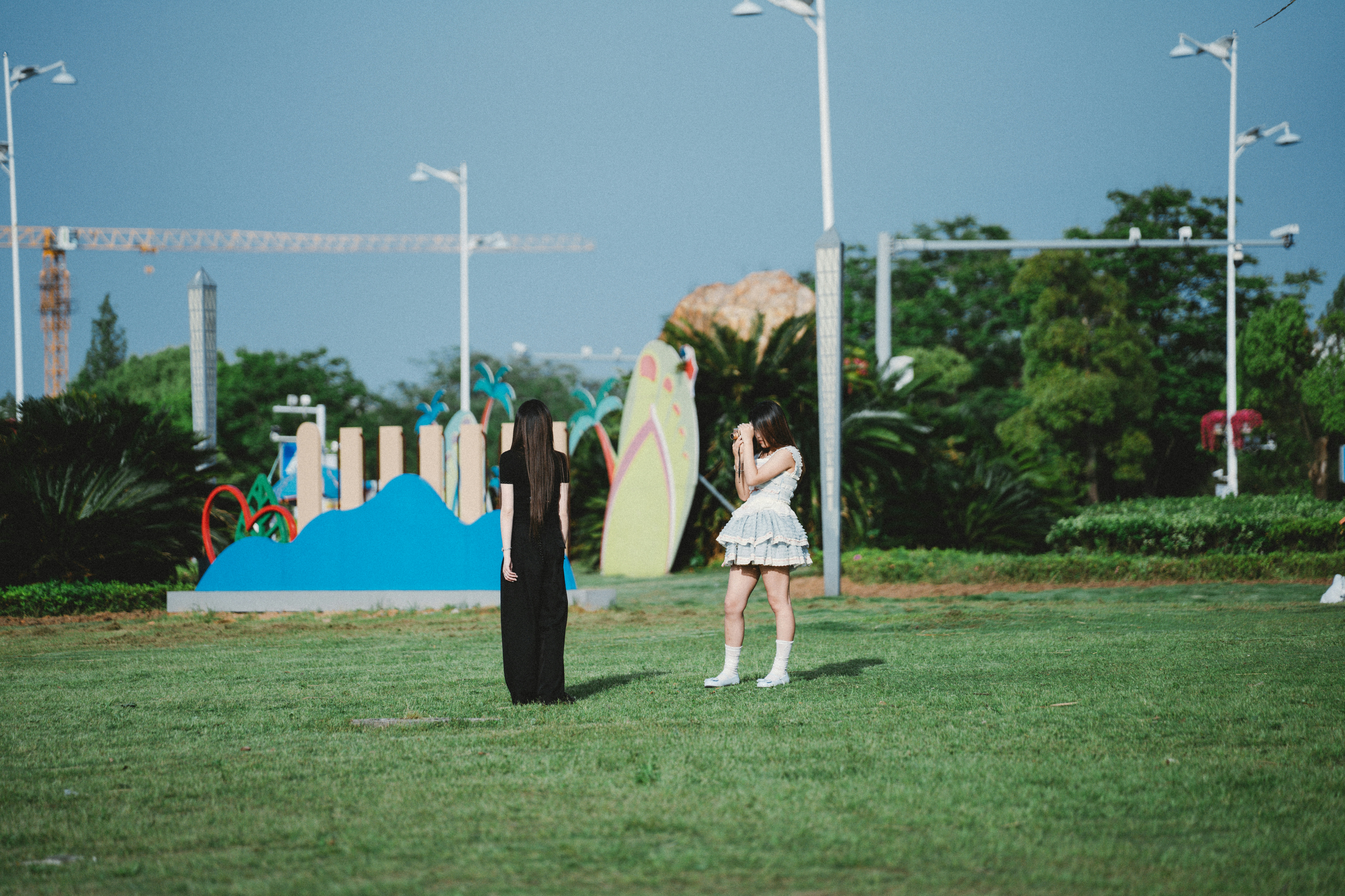 Two figures in a sunlit park engage in a quiet moment near colorful playground art