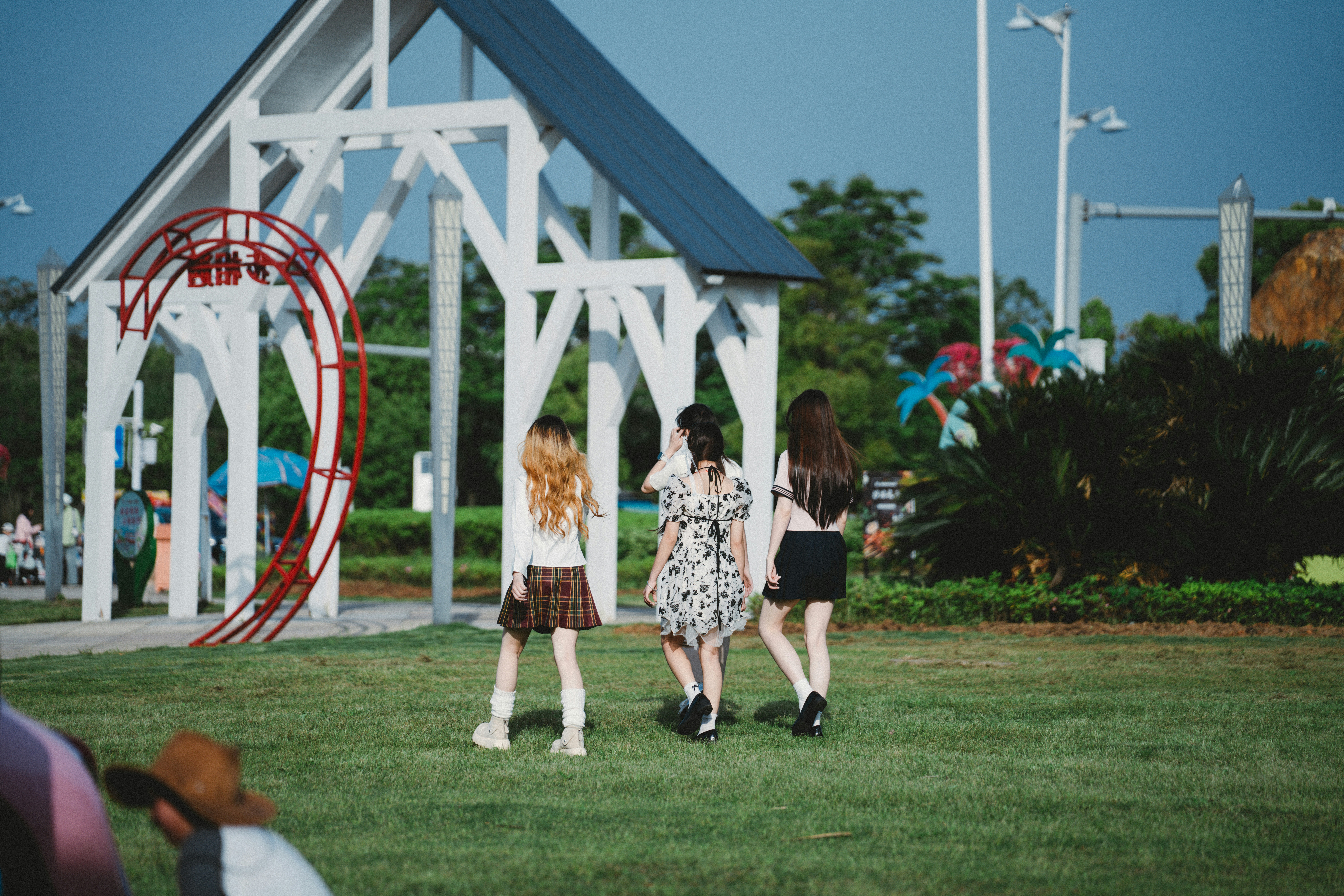 Three Friends Walk Under a White Pavilion in a Sunny Park