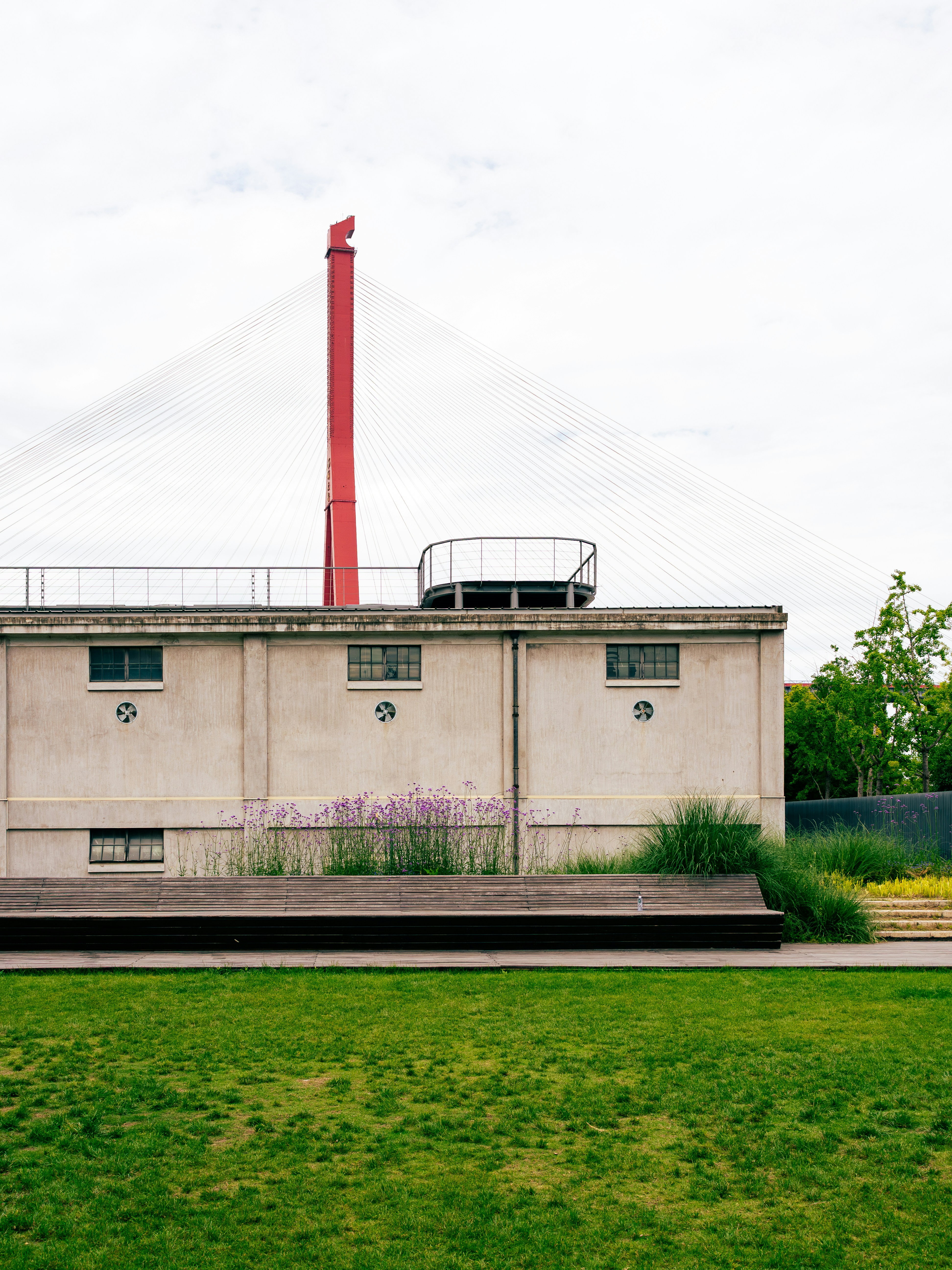 Red Cable-Stayed Tower Rising Behind a Quiet Concrete Building