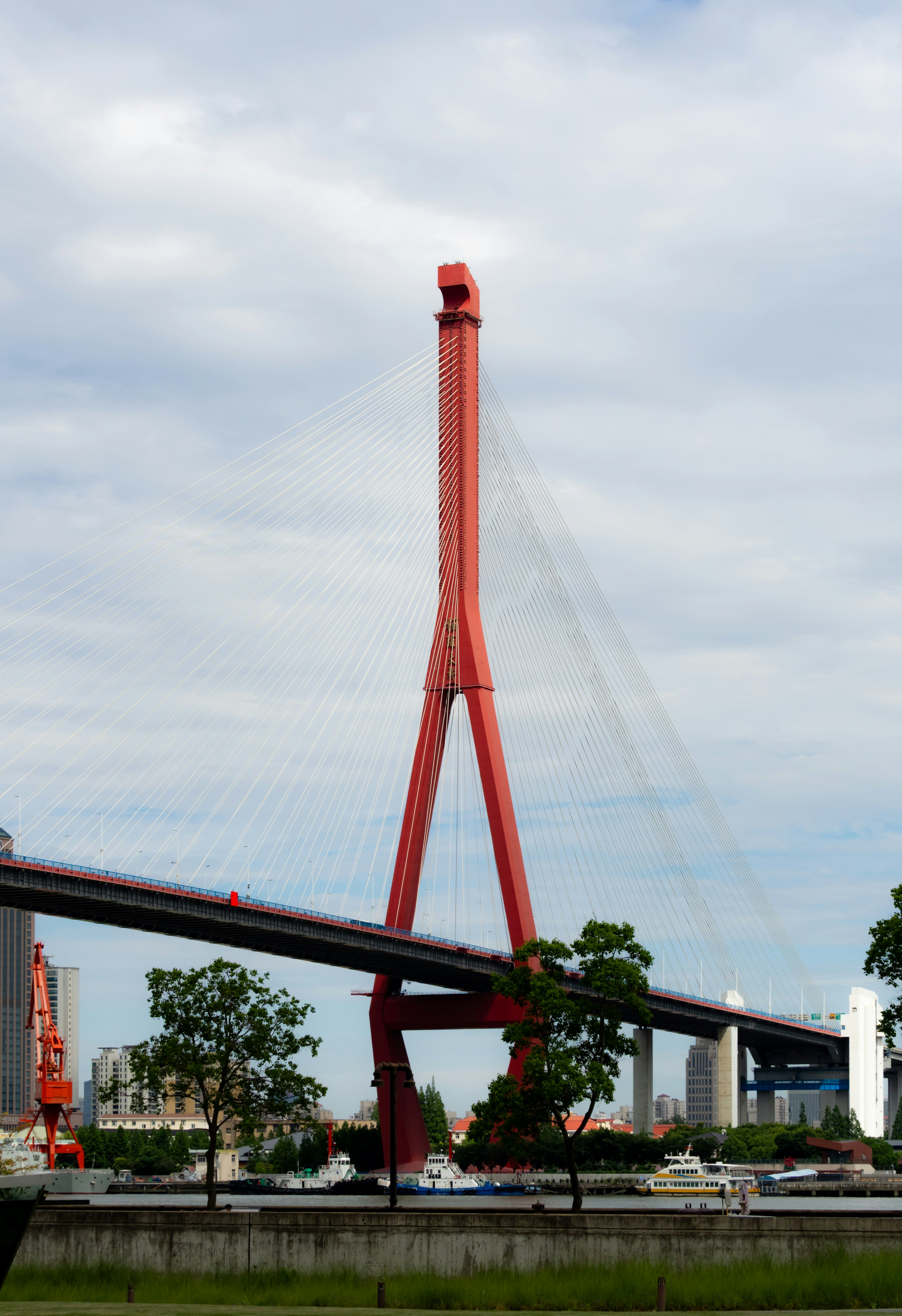 A striking red cable-stayed bridge spans over a river.