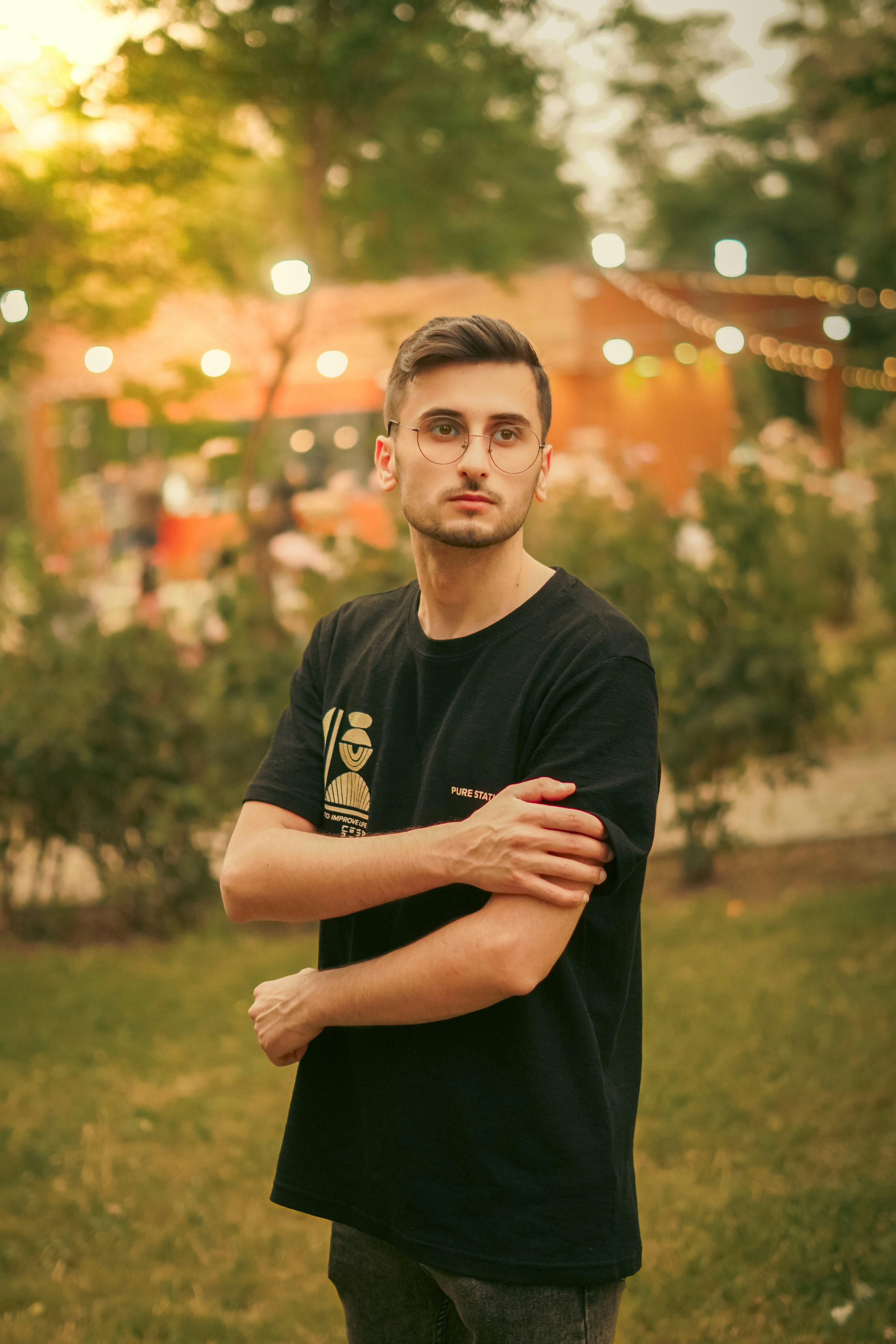 Young man in glasses standing outdoors with arms crossed.