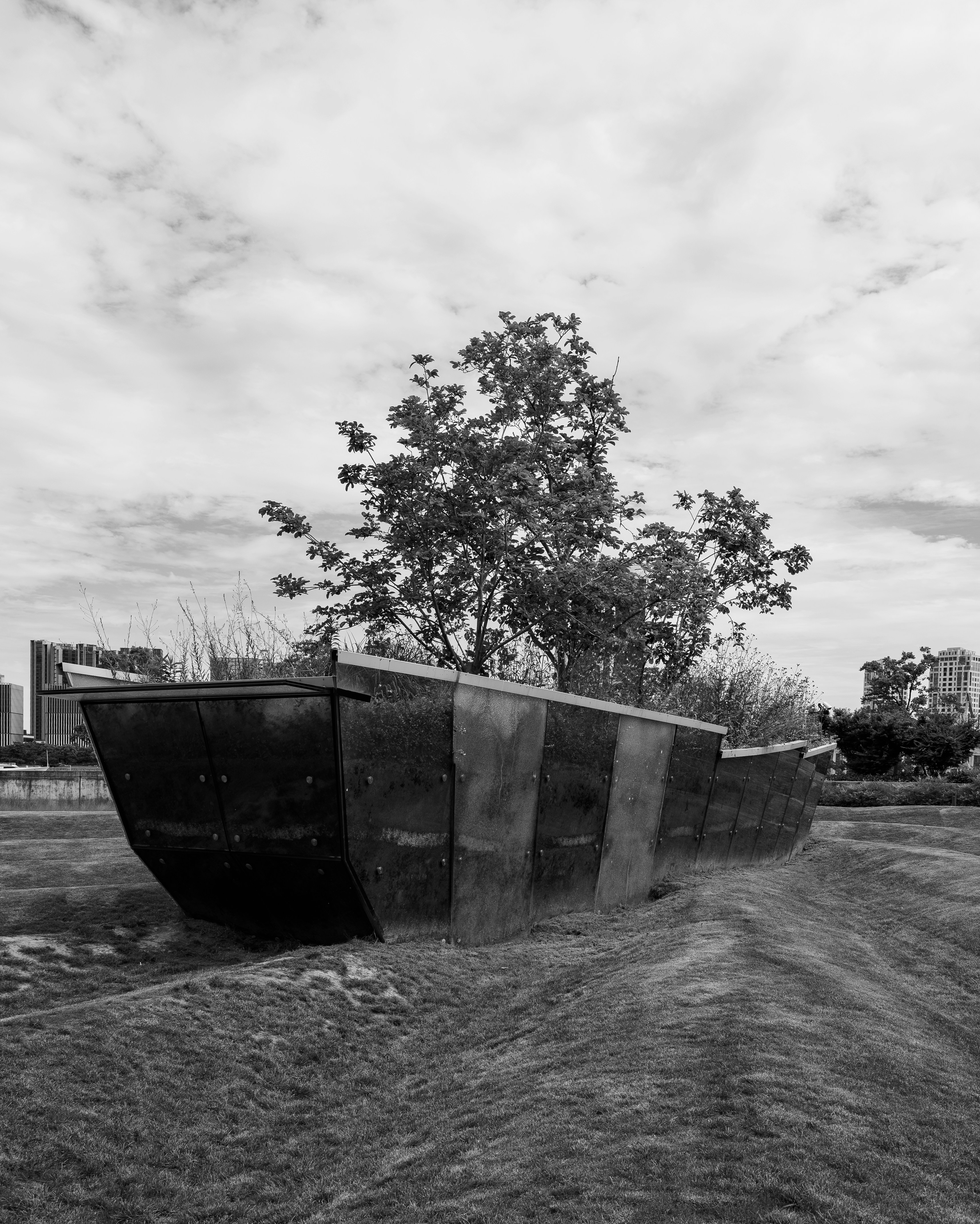 Industrial sculpture curves into a windswept park, framed by distant urban silhouettes