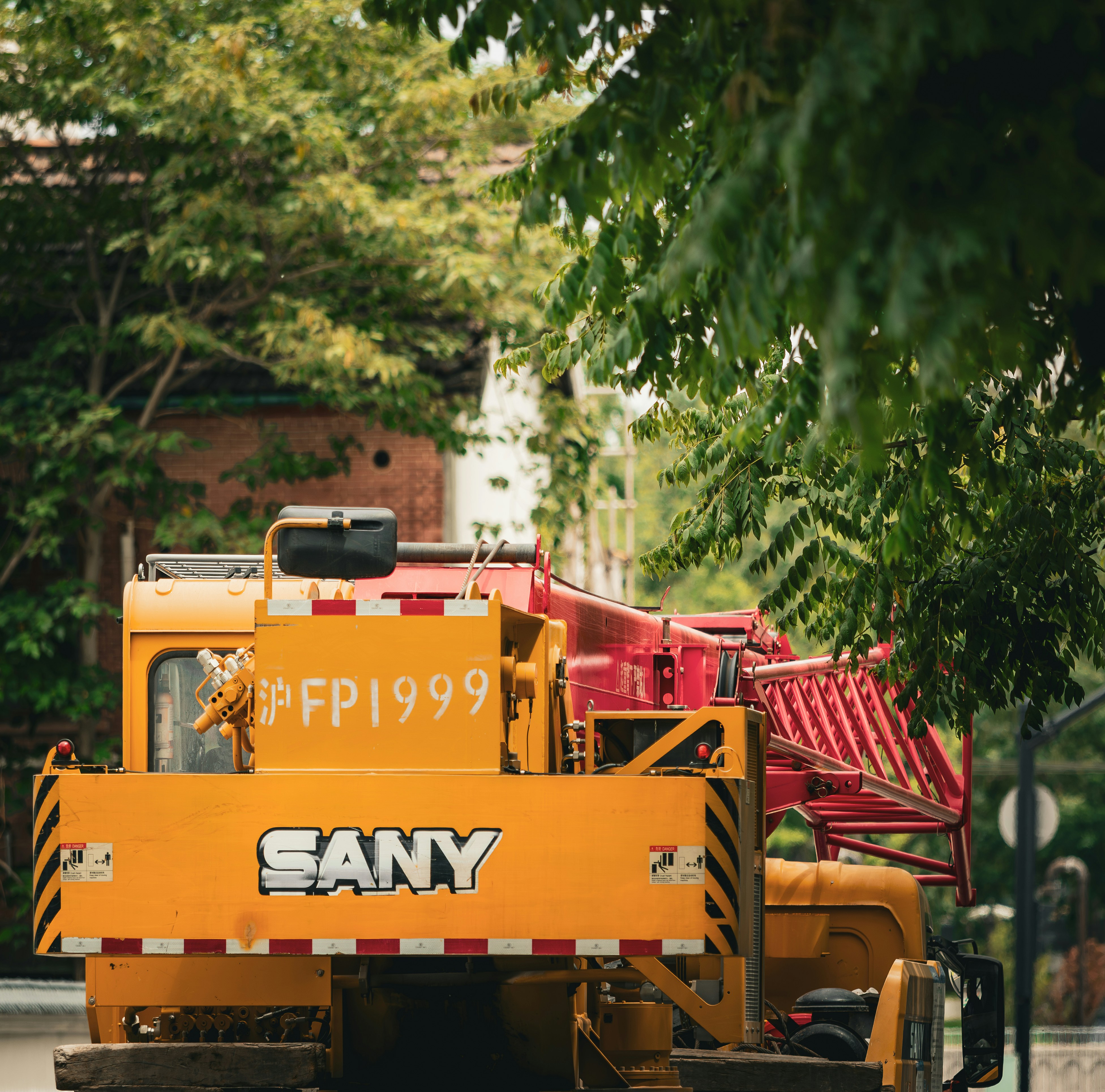 Bright Yellow SANY Crane at Rest Under a Canopy of Greenery