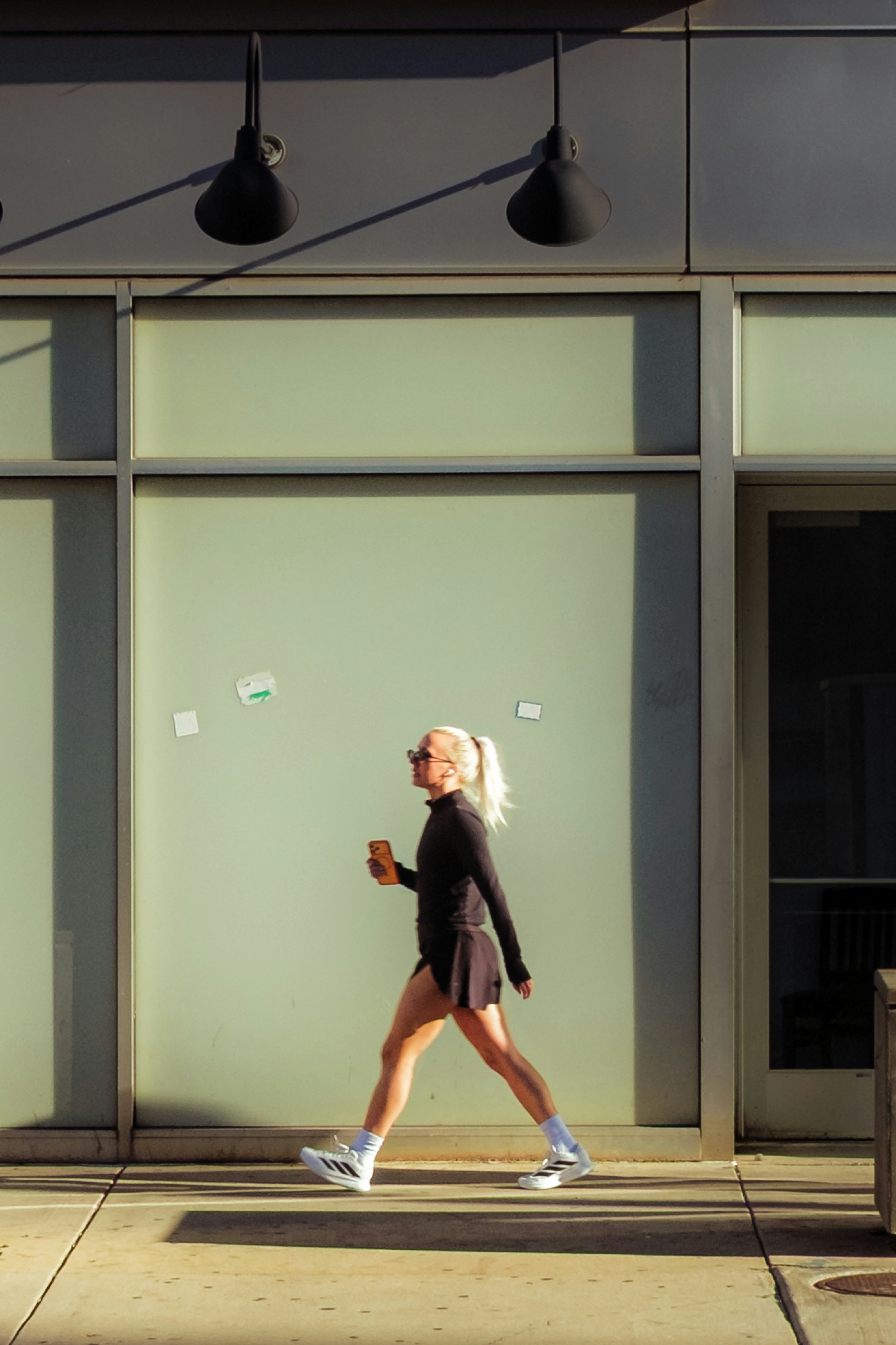 Runner in black dress: sunlight, motion, and storefront geometry