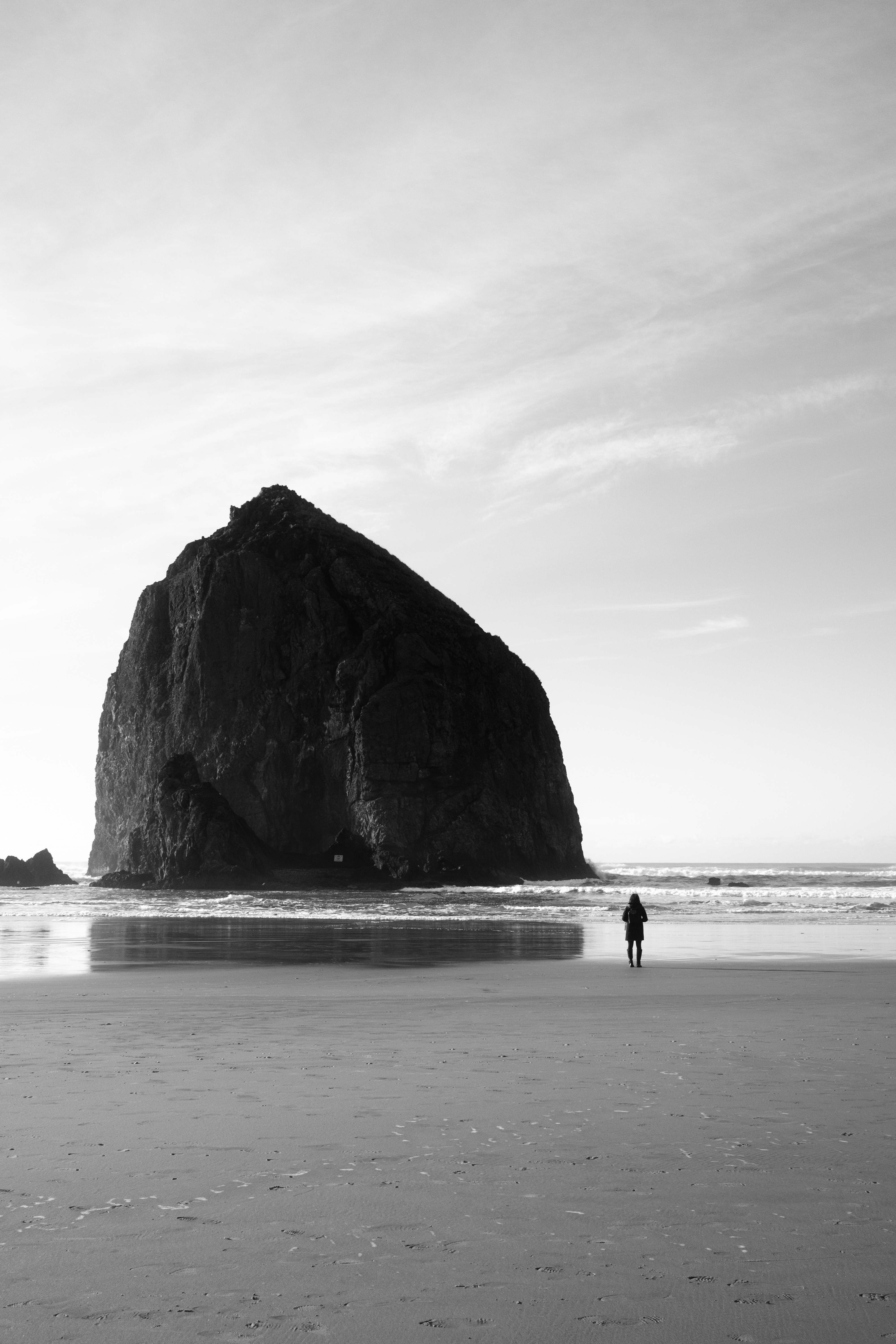  lone figure at the edge of the sea beside a colossal sea stack