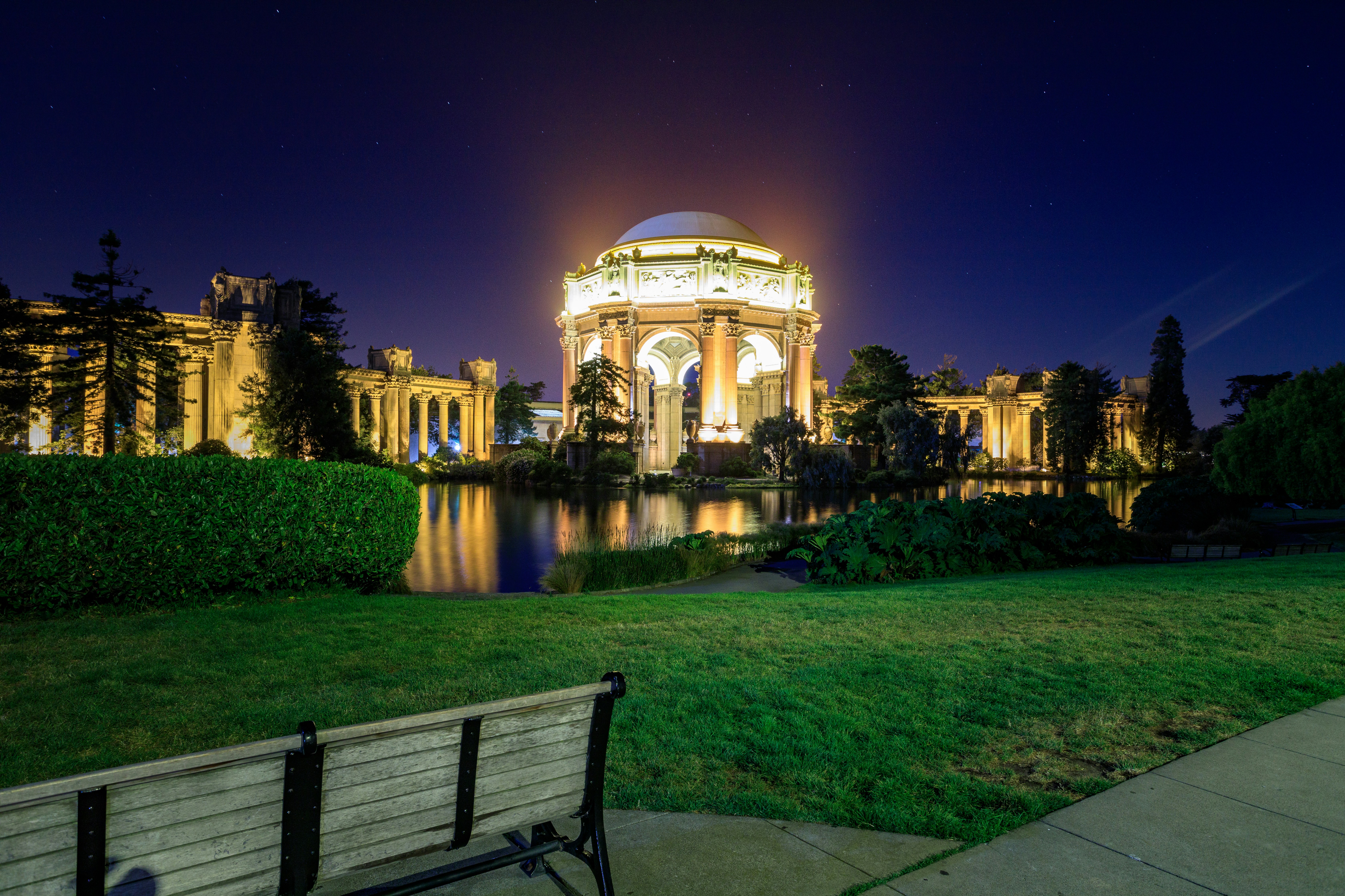 Illuminated palace with dome reflected in water at night.