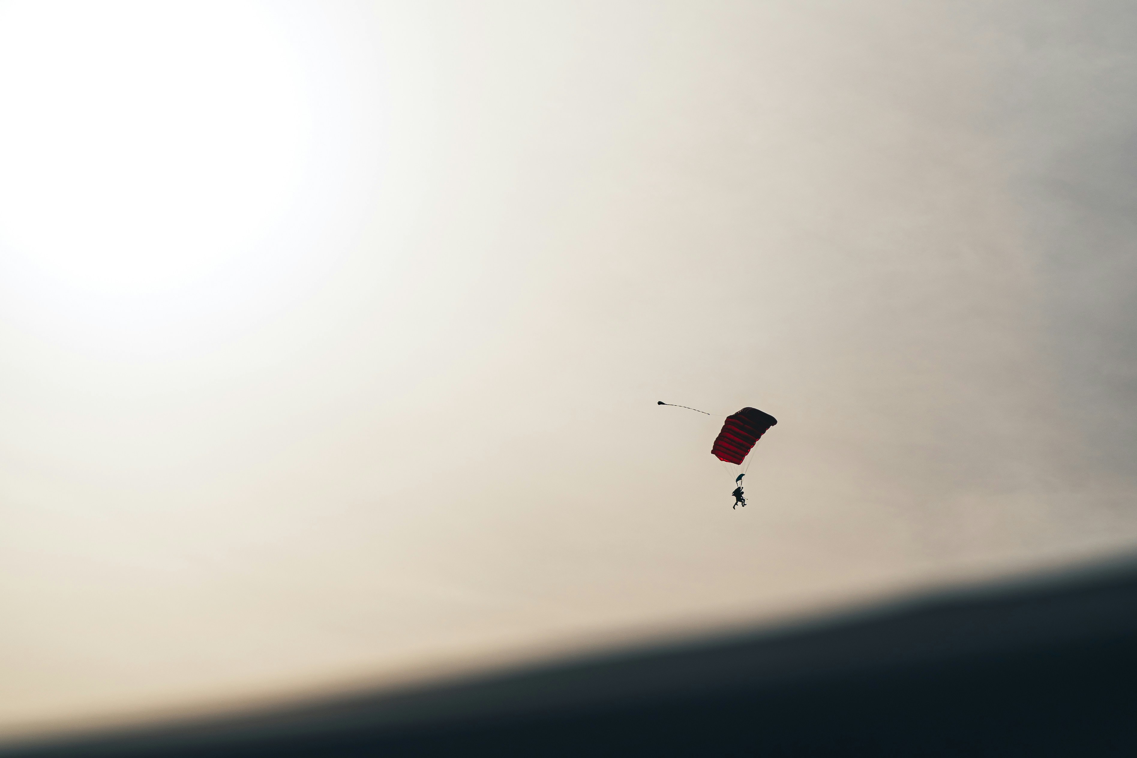 Floating Silhouette: Parachute Descent Across a Backlit Horizon
