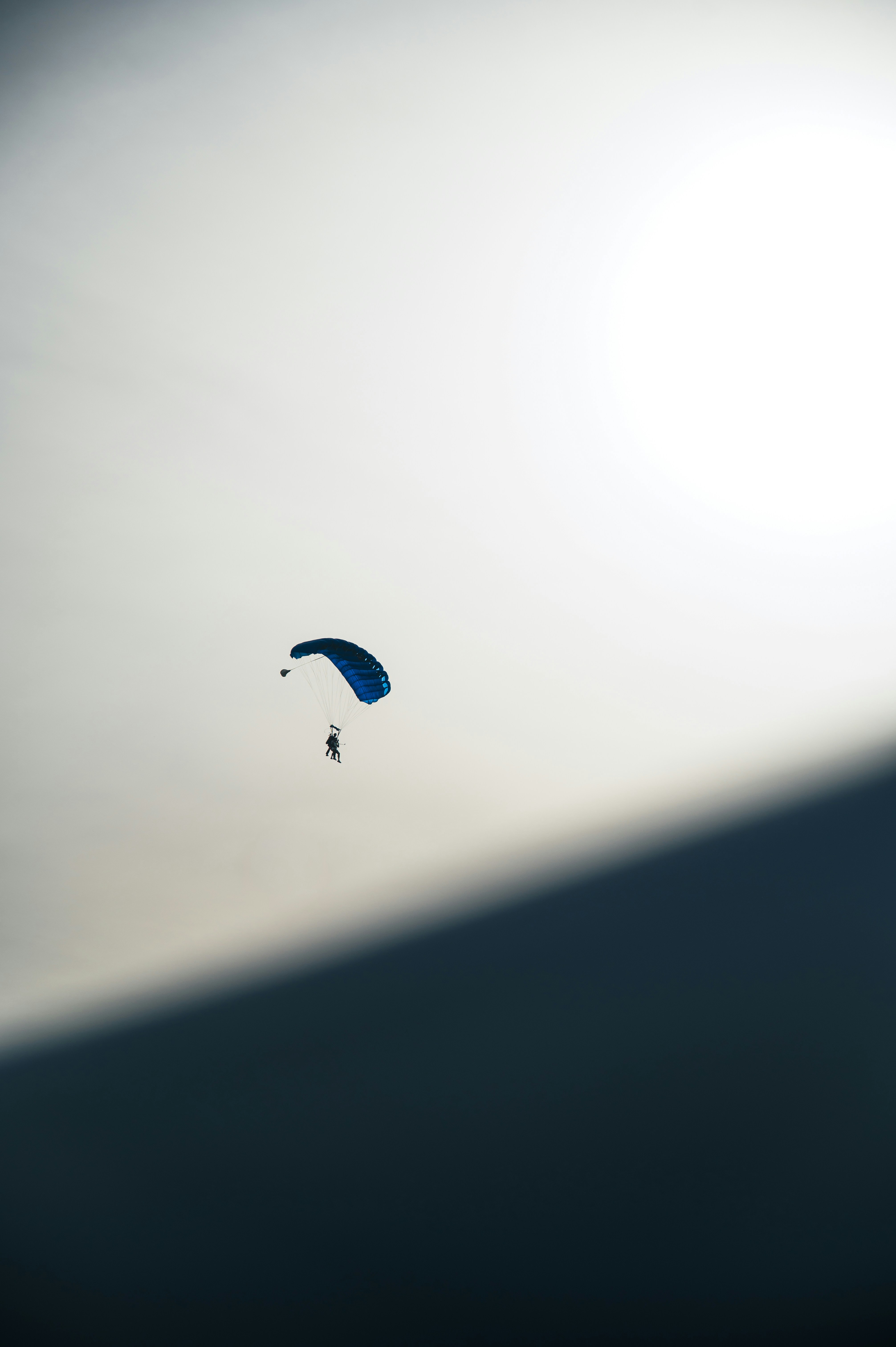 A person paragliding with a blue canopy in the sky.