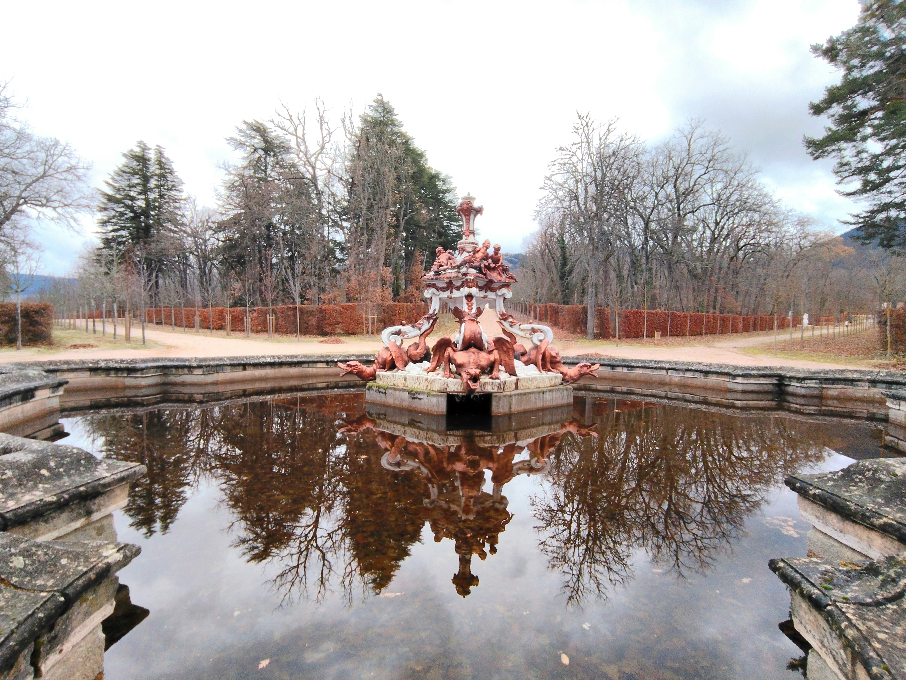 Symmetric fountain sculpture mirrored in calm basin under winter trees