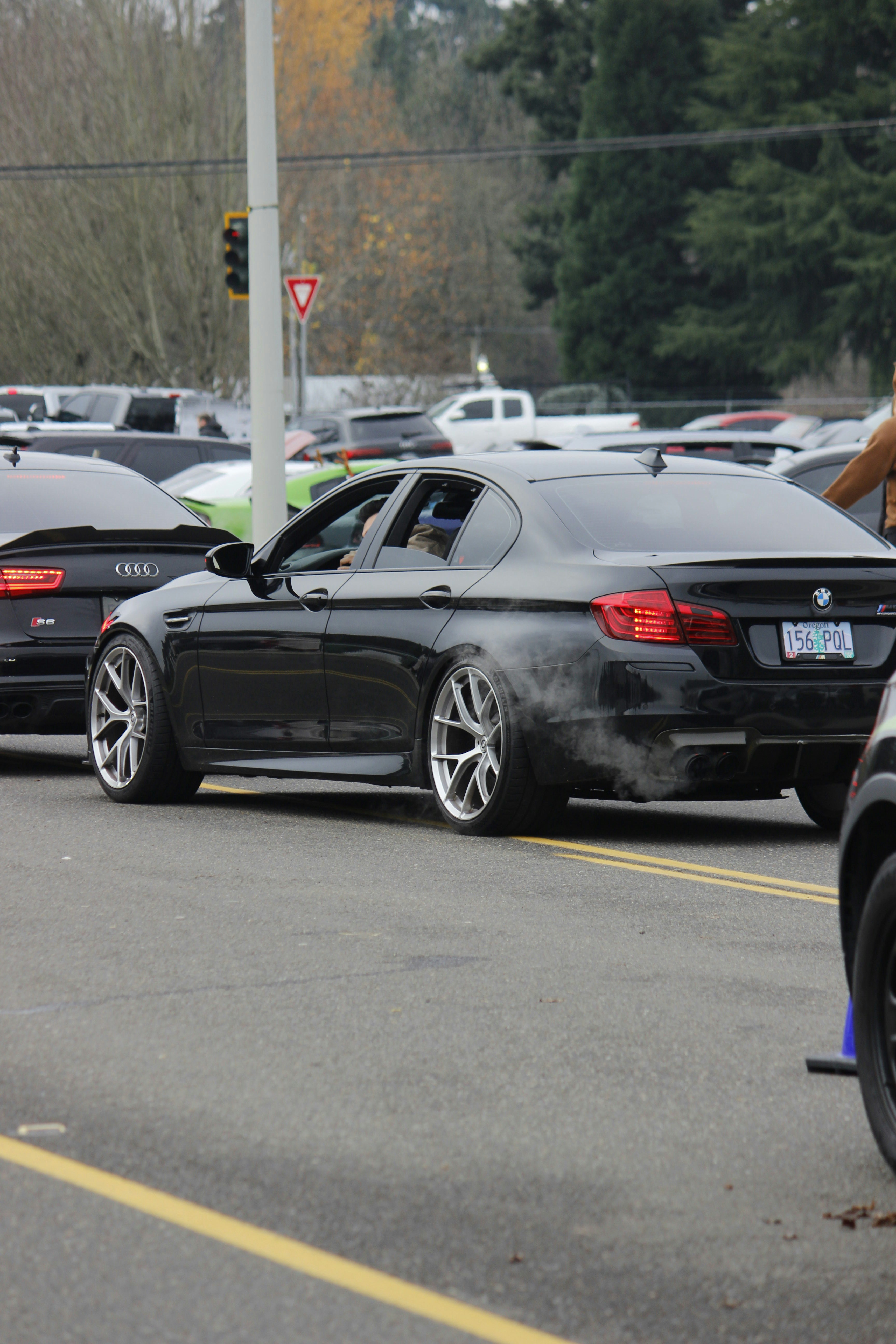 Black sedan drifting smoke in a busy parking lot during a car meet