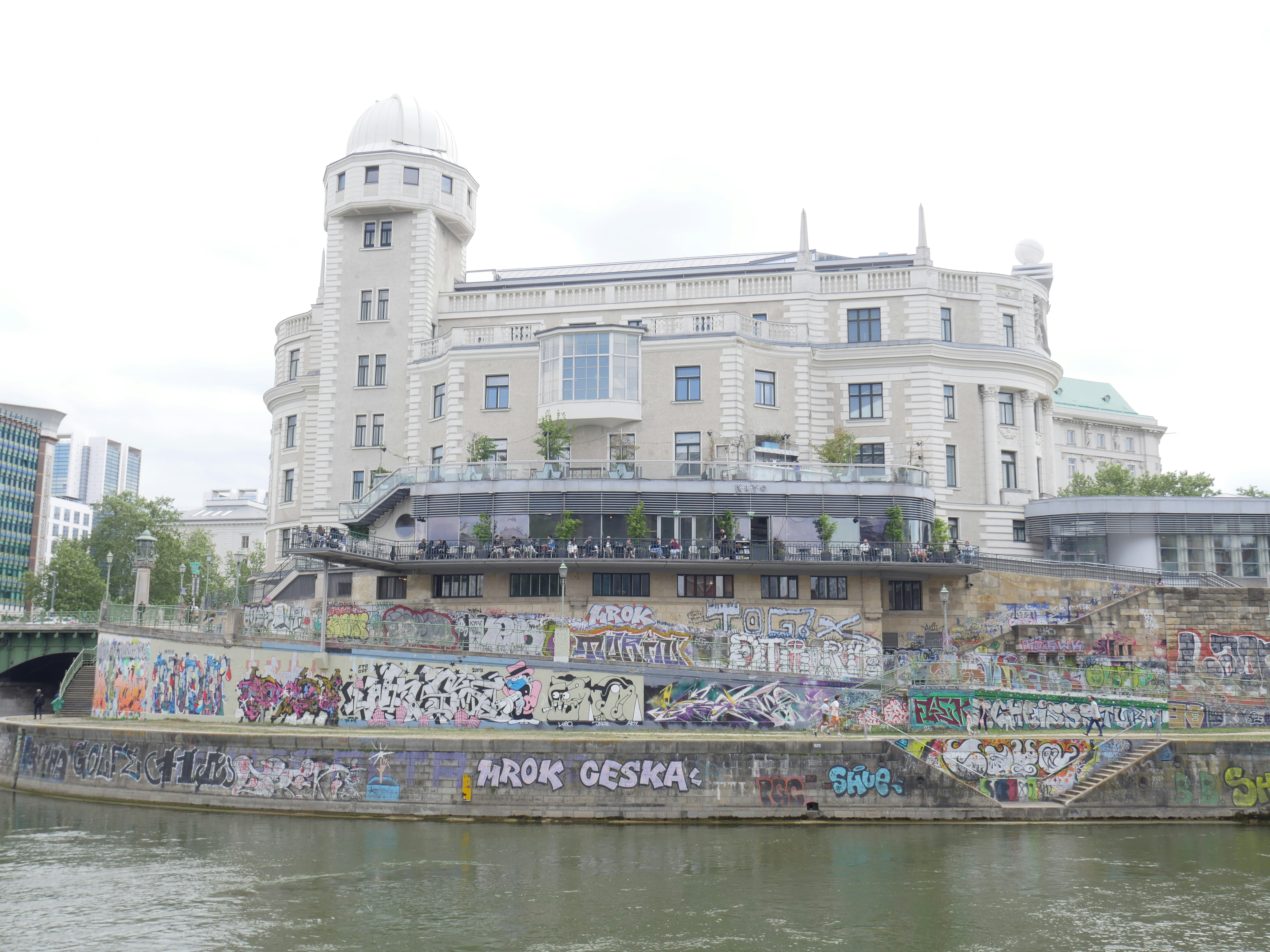 Riverside fortress: a graffitied embankment beneath a grand stone facade